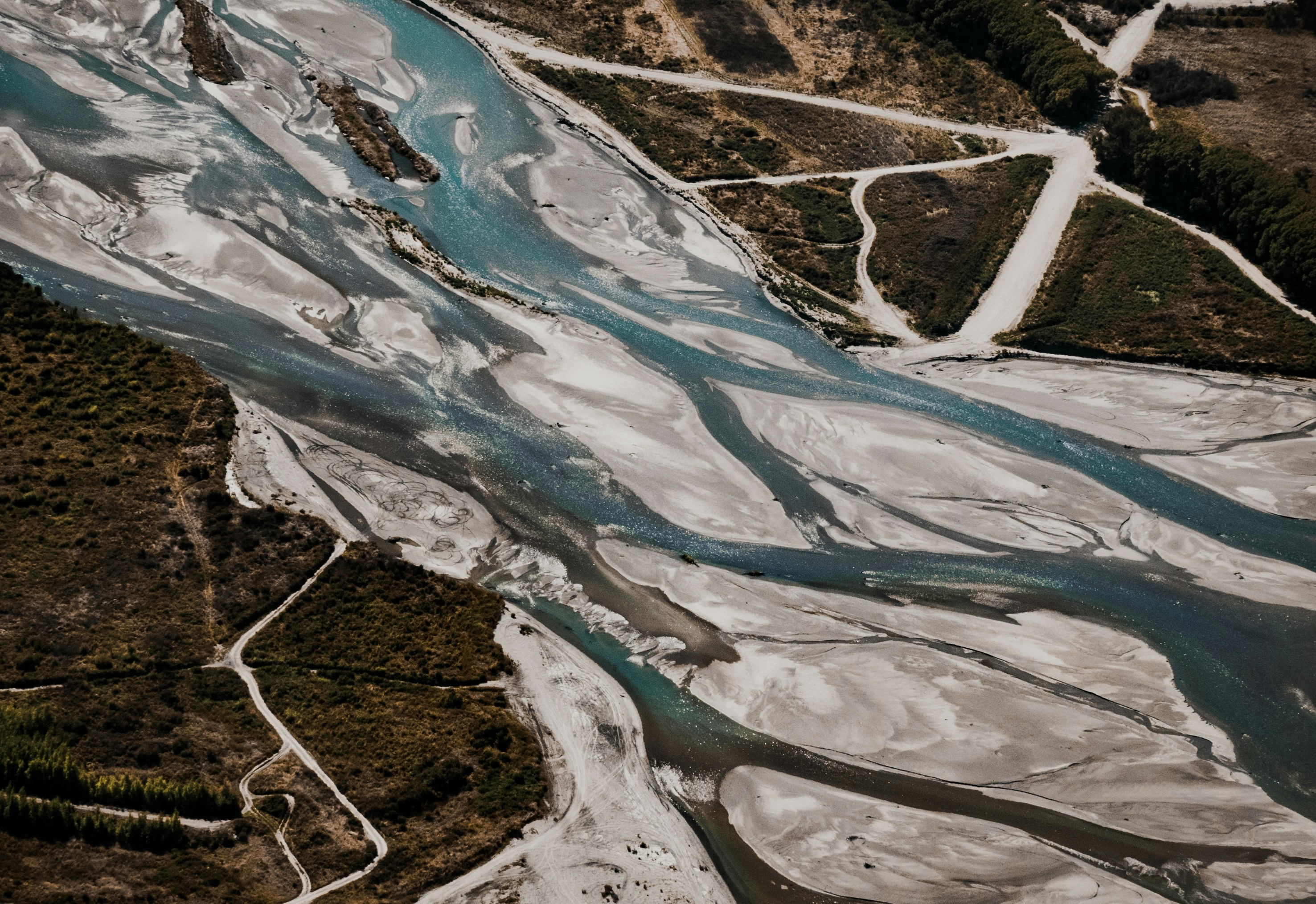 Aerial view of a braided river with turquoise waters weaving through sandy banks and lush patches of greenery.