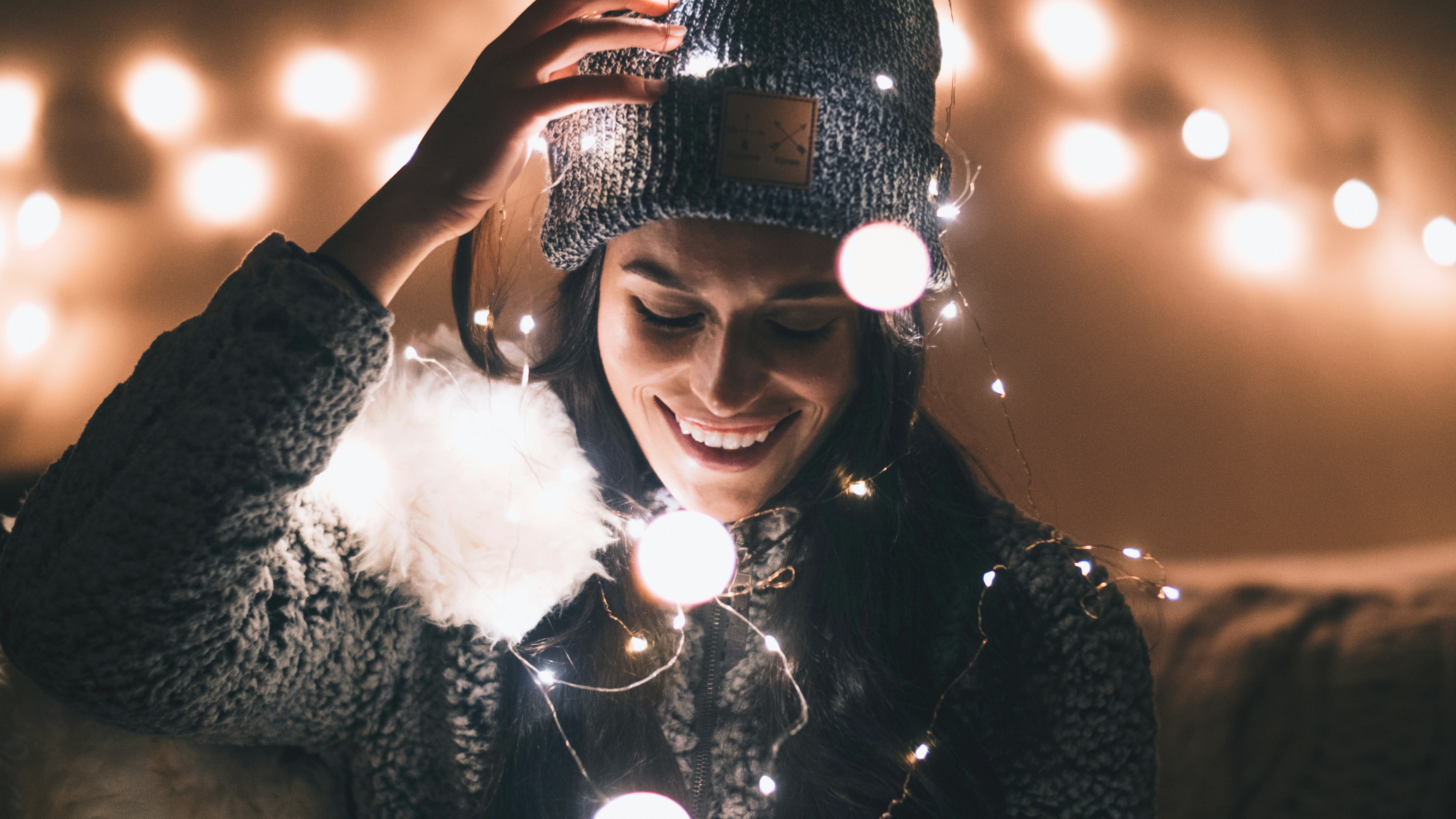 Person surrounded by glowing string lights, wearing a cozy hat and jacket.