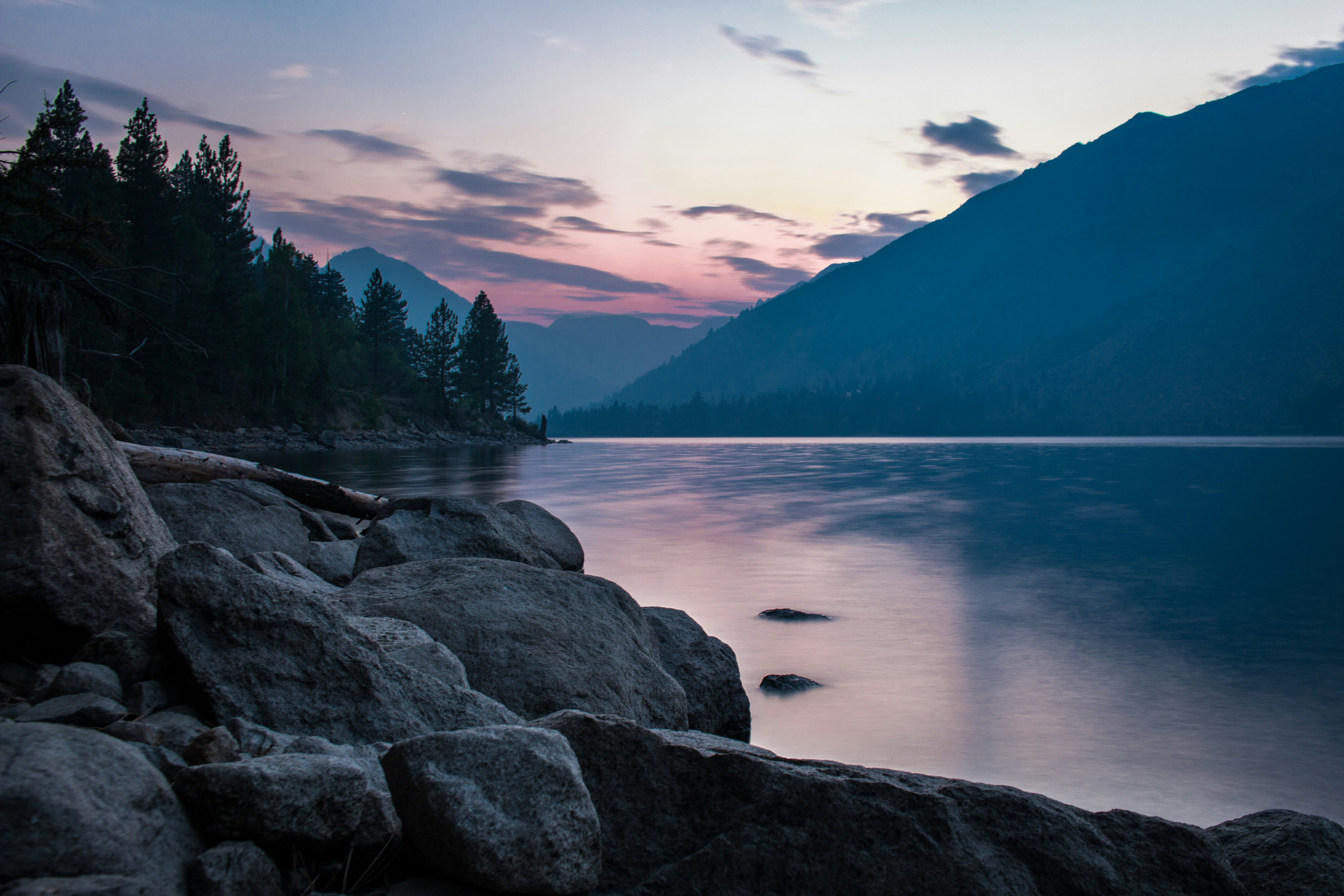 Gentle waves lapping against a rocky shoreline under a twilight sky, with mountains silhouetted in the background.