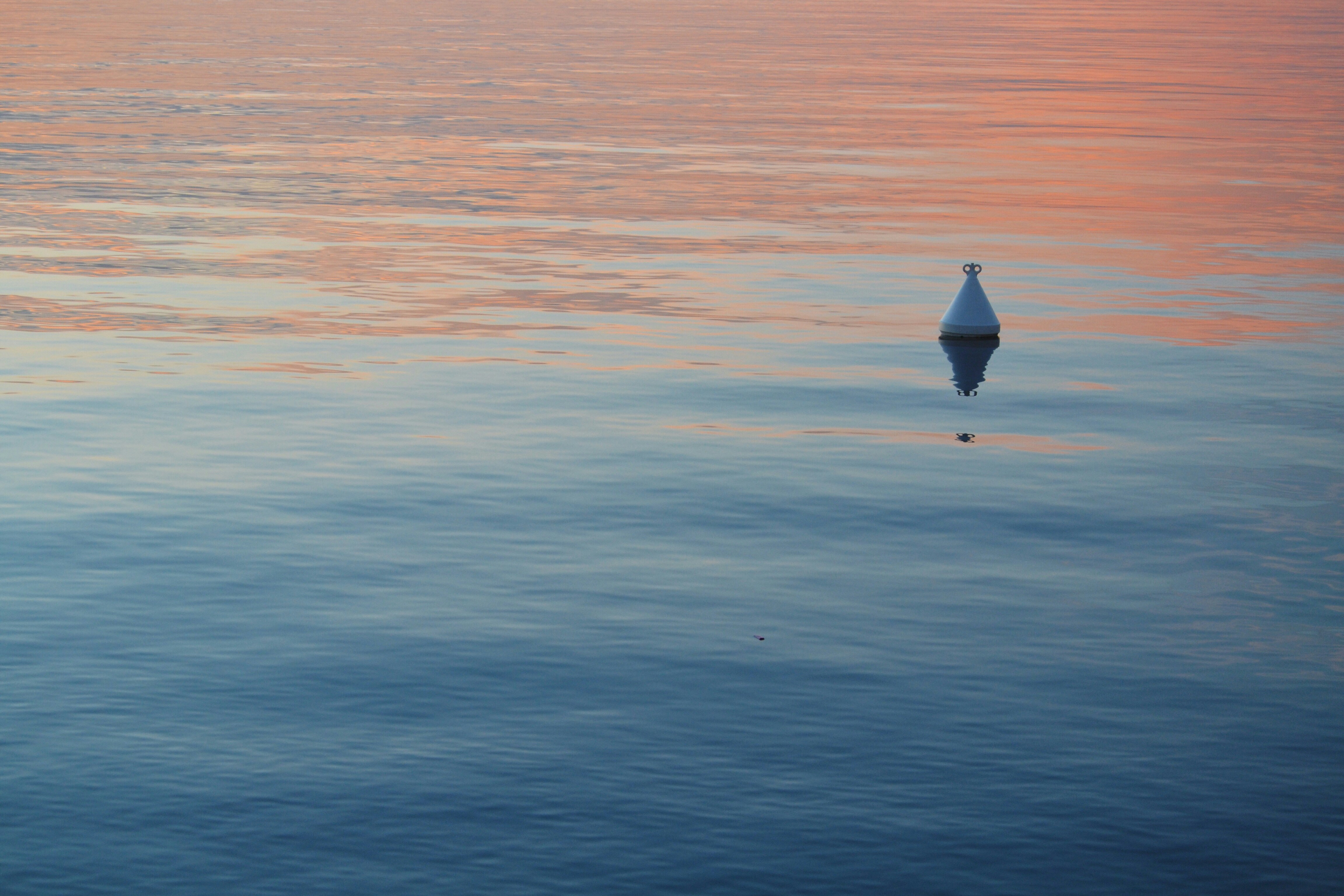 A solitary buoy reflected on calm waters, surrounded by soft hues of dusk. The tranquil scene captures the essence of peaceful solitude.