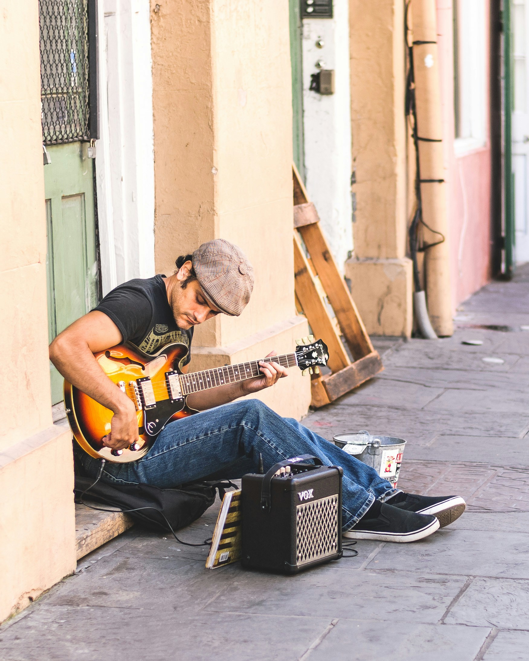 A guitarist seated on the sidewalk, passionately playing his instrument while an amplifier sits beside him. The scene captures the essence of street music culture.