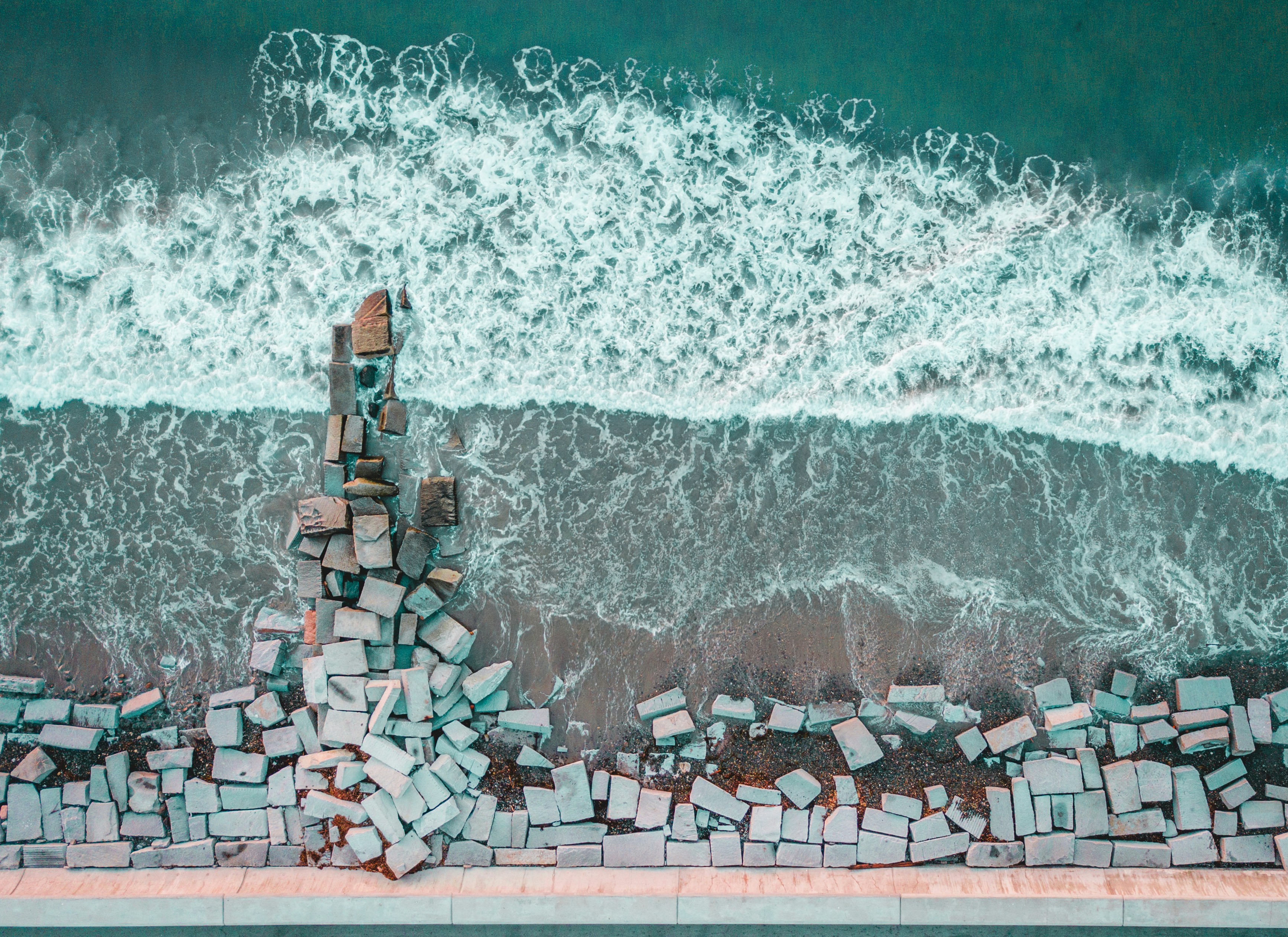 Aerial view of stone blocks arranged along a shoreline with waves crashing against them.
