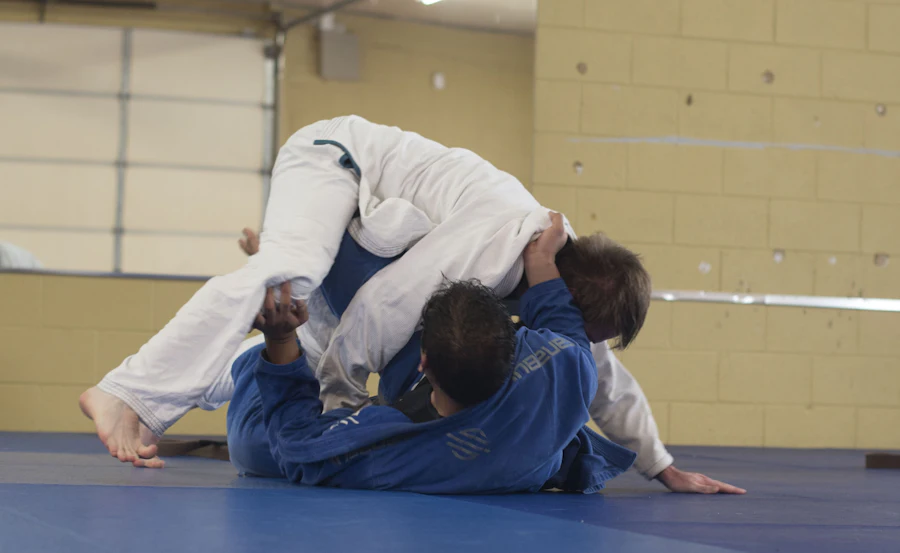 Two martial artists engage in a dynamic grappling exchange on a blue mat in a gym setting.