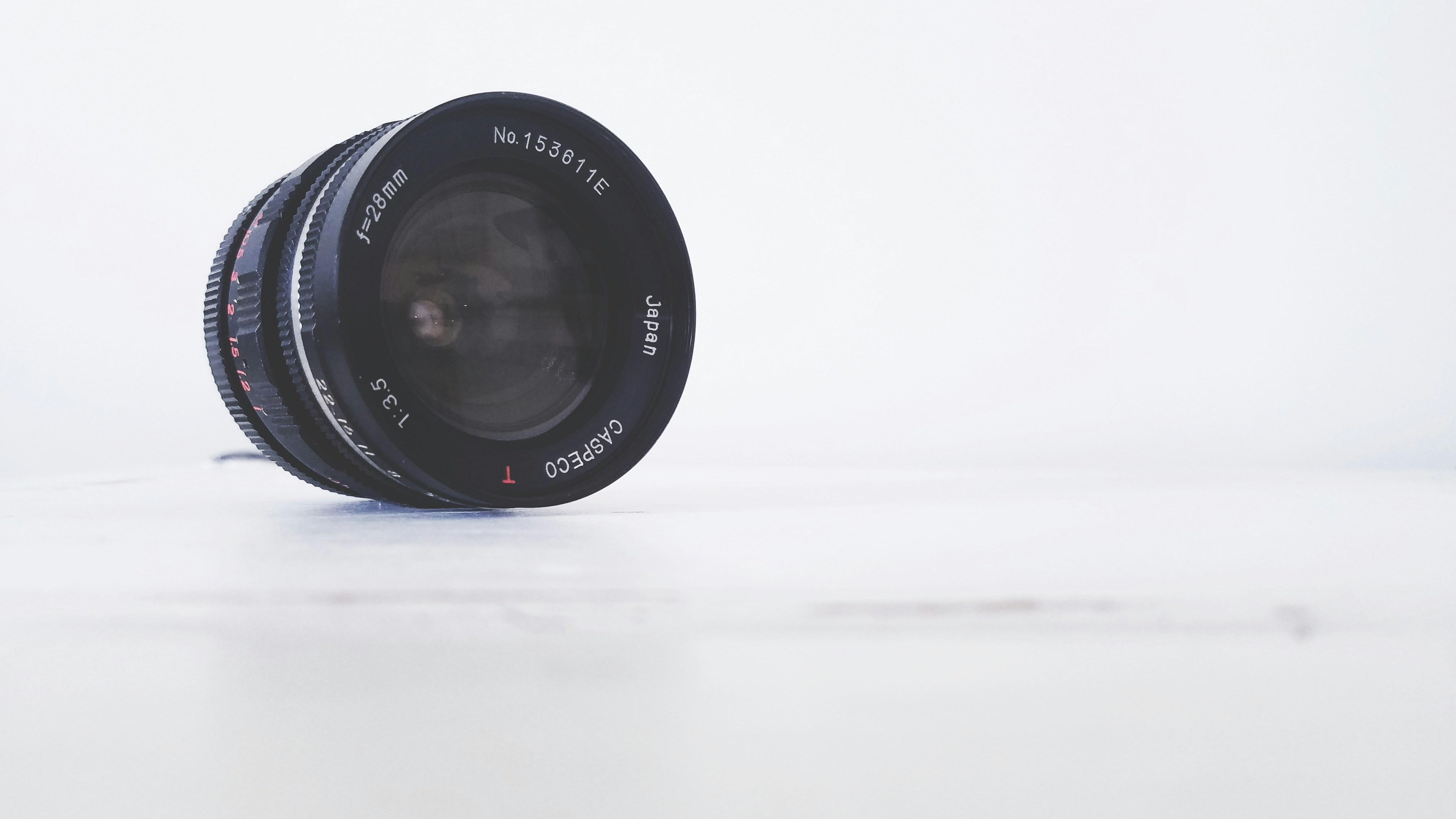 Camera lens resting on a clean white surface with a minimalistic backdrop.