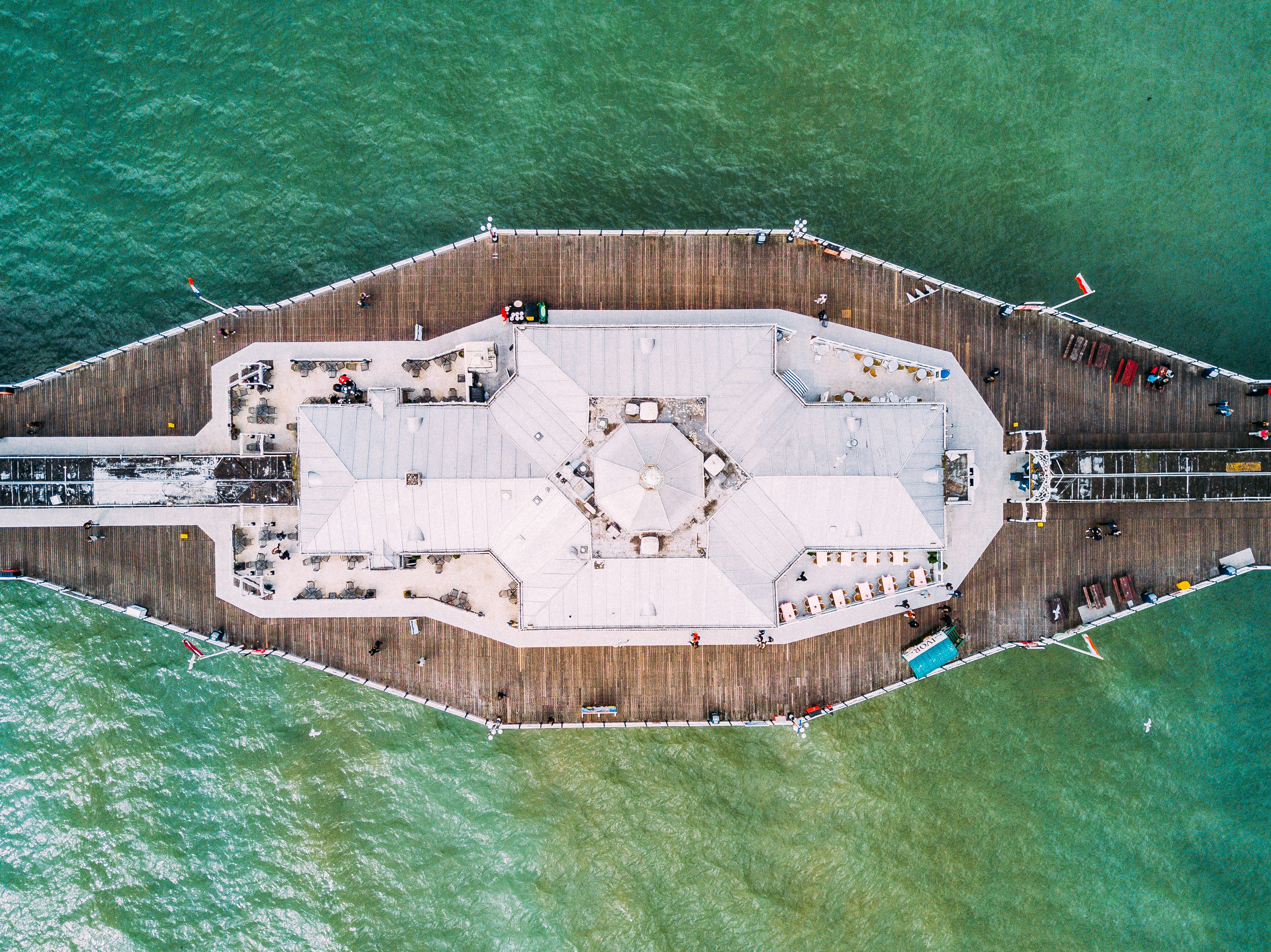 Aerial view of a pier featuring a hexagonal structure with seating areas, surrounded by tranquil turquoise waters.
