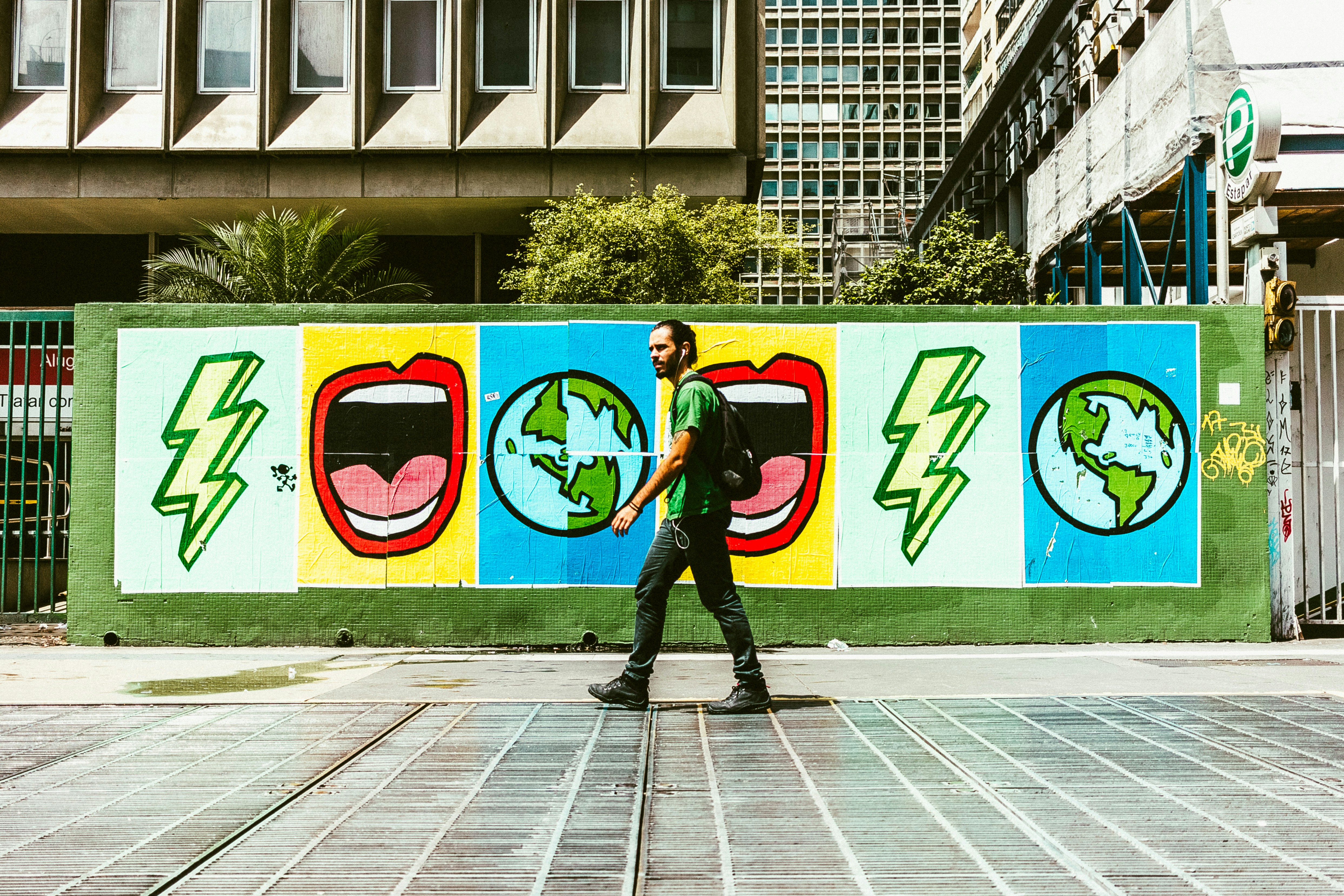 Man walking past a colorful graffiti wall featuring lightning bolts, mouths, and globes.