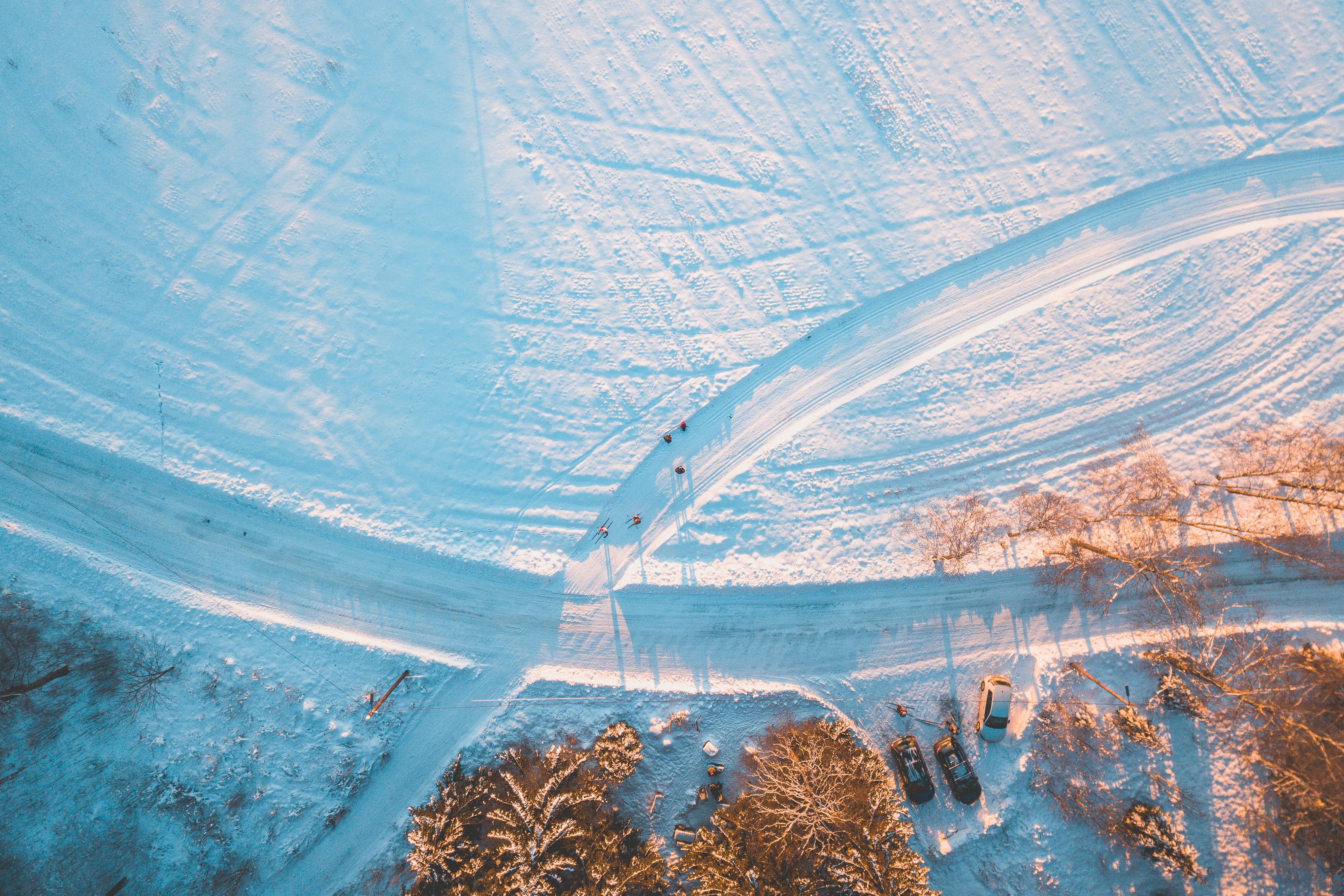 Aerial view of a snowy landscape featuring winding paths and bare trees, capturing the tranquility of winter. The scene highlights the contrast between the white snow and the dark tree line.