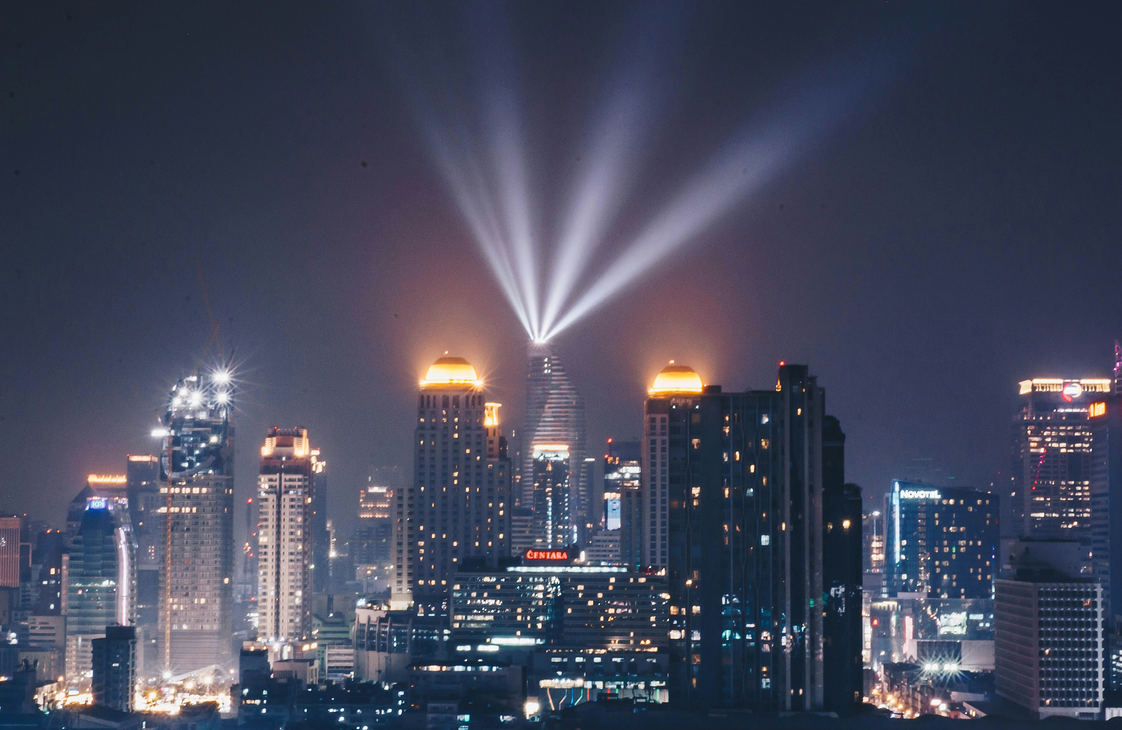 City skyscrapers illuminated by bright spotlights under a night sky.