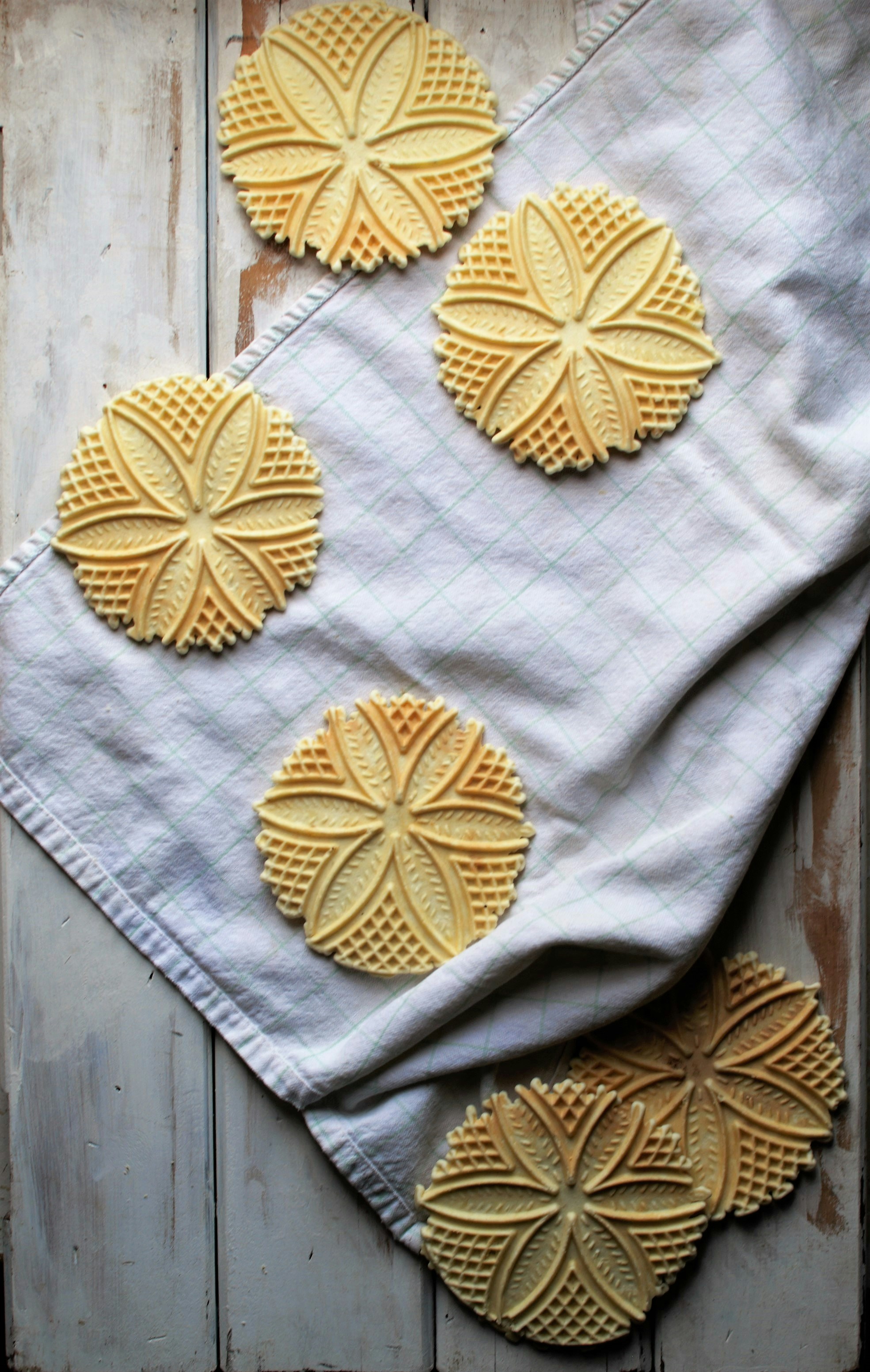 Round butter cookies with embossed star patterns rest on a light linen cloth laid over a weathered wooden surface. The arrangement emphasizes texture and geometry of the cookies.