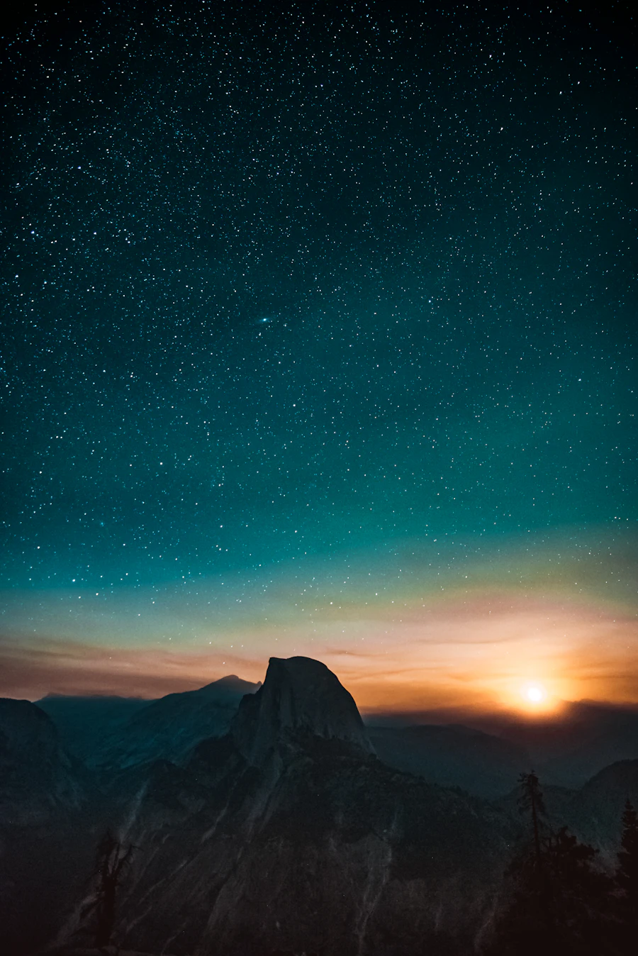 Silhouetted mountain peak under a star-filled night sky, with a warm sunrise glow on the horizon.