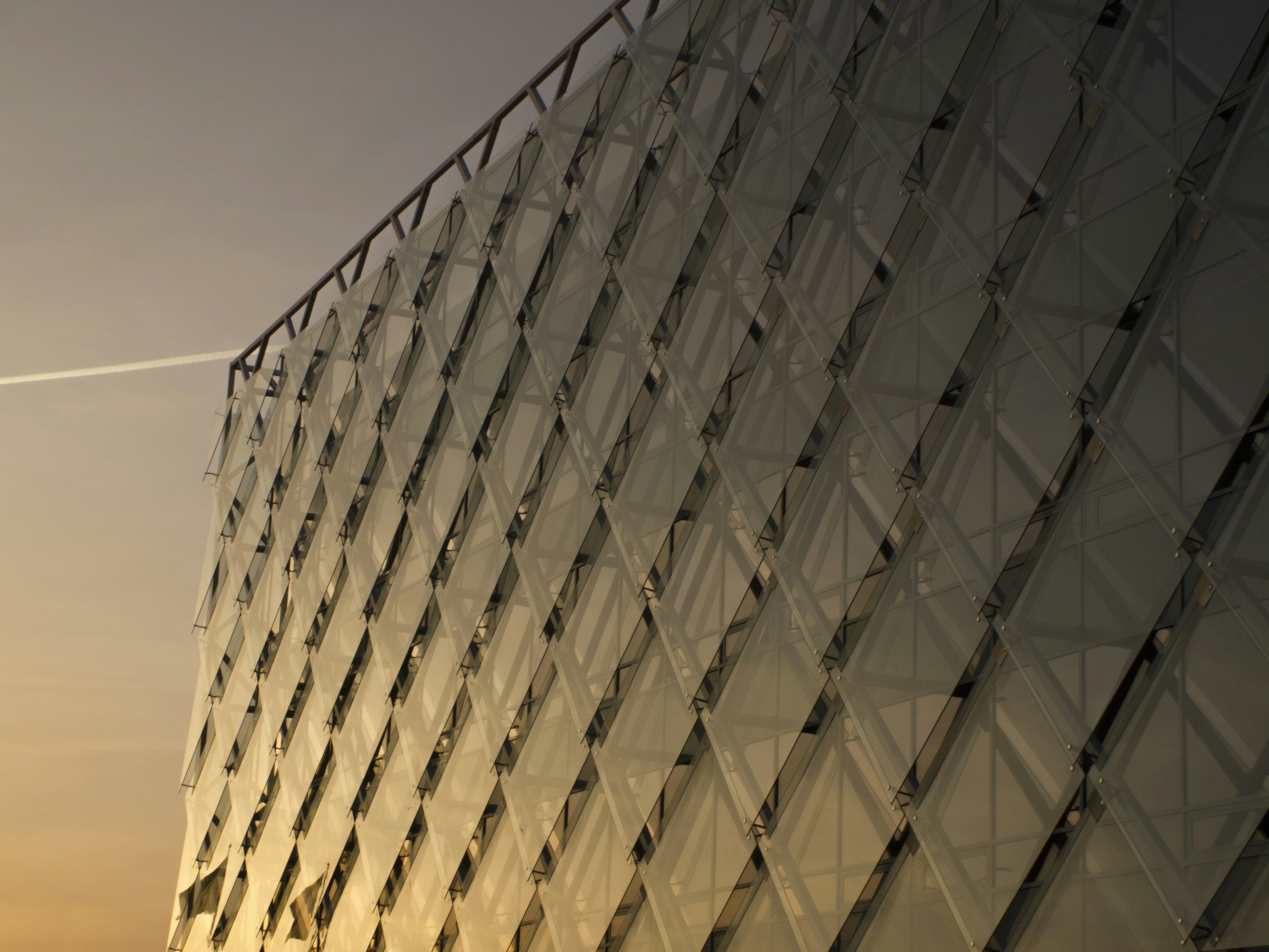 Glass facade of a modern building reflecting the warm hues of a sunset sky.