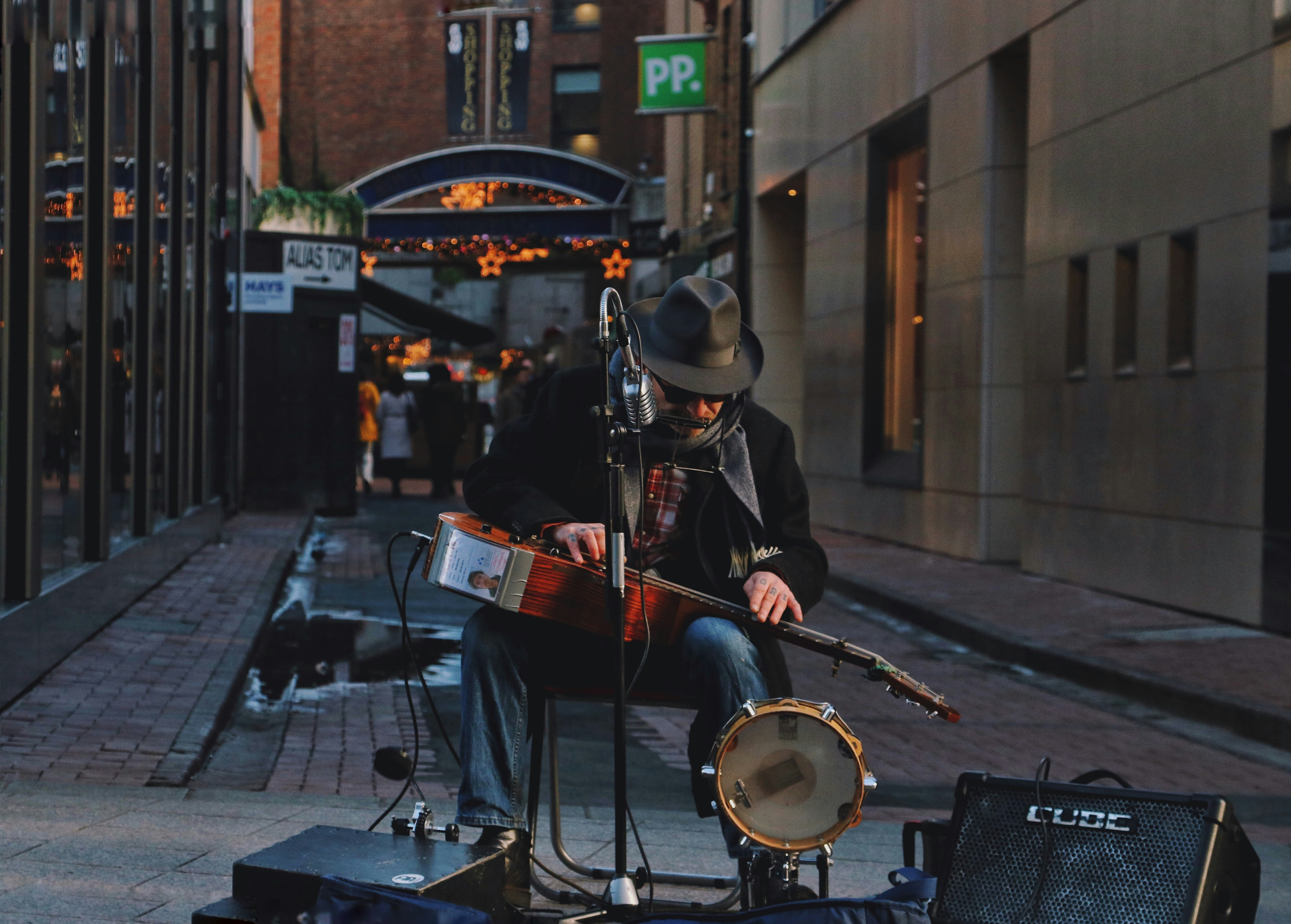 Street performer playing multiple instruments in a narrow urban alleyway.