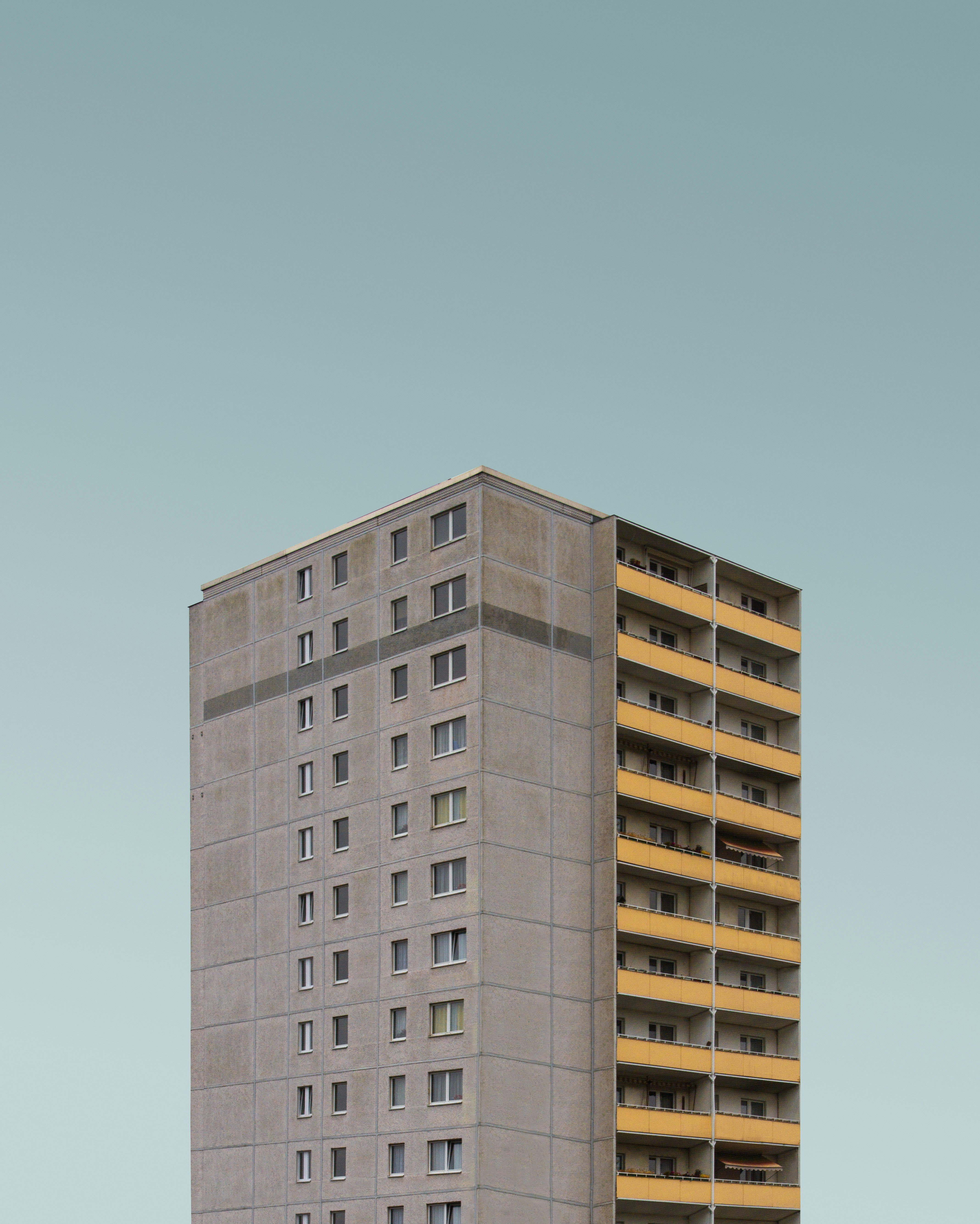 A tall, concrete apartment building stands prominently against a soft, pastel sky, showcasing its stark architectural lines and minimalist design.