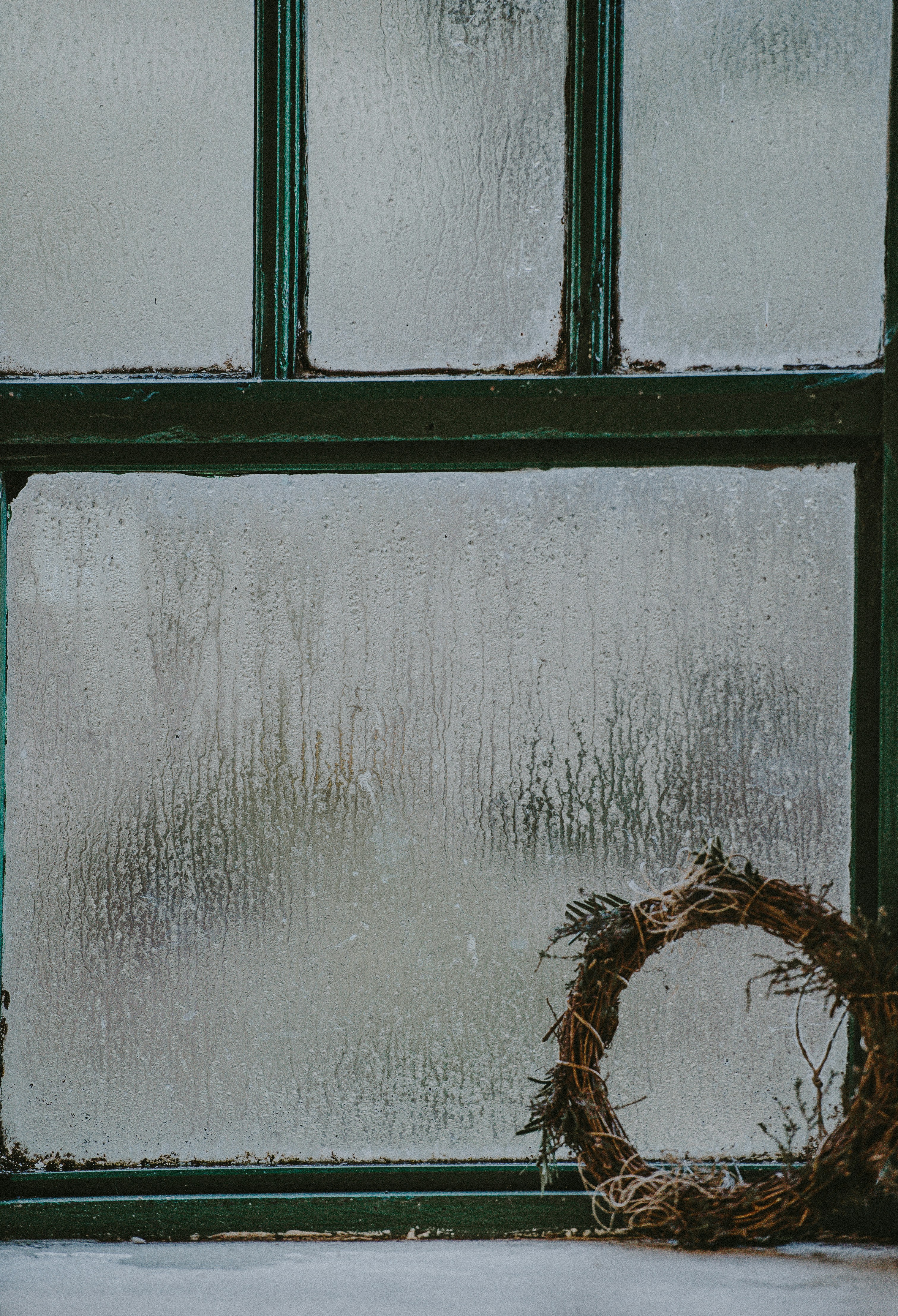 Frosted window panes create a soft backdrop for a rustic wreath, evoking a sense of warmth amidst the chill. The interplay of glass and greenery adds a touch of serenity.