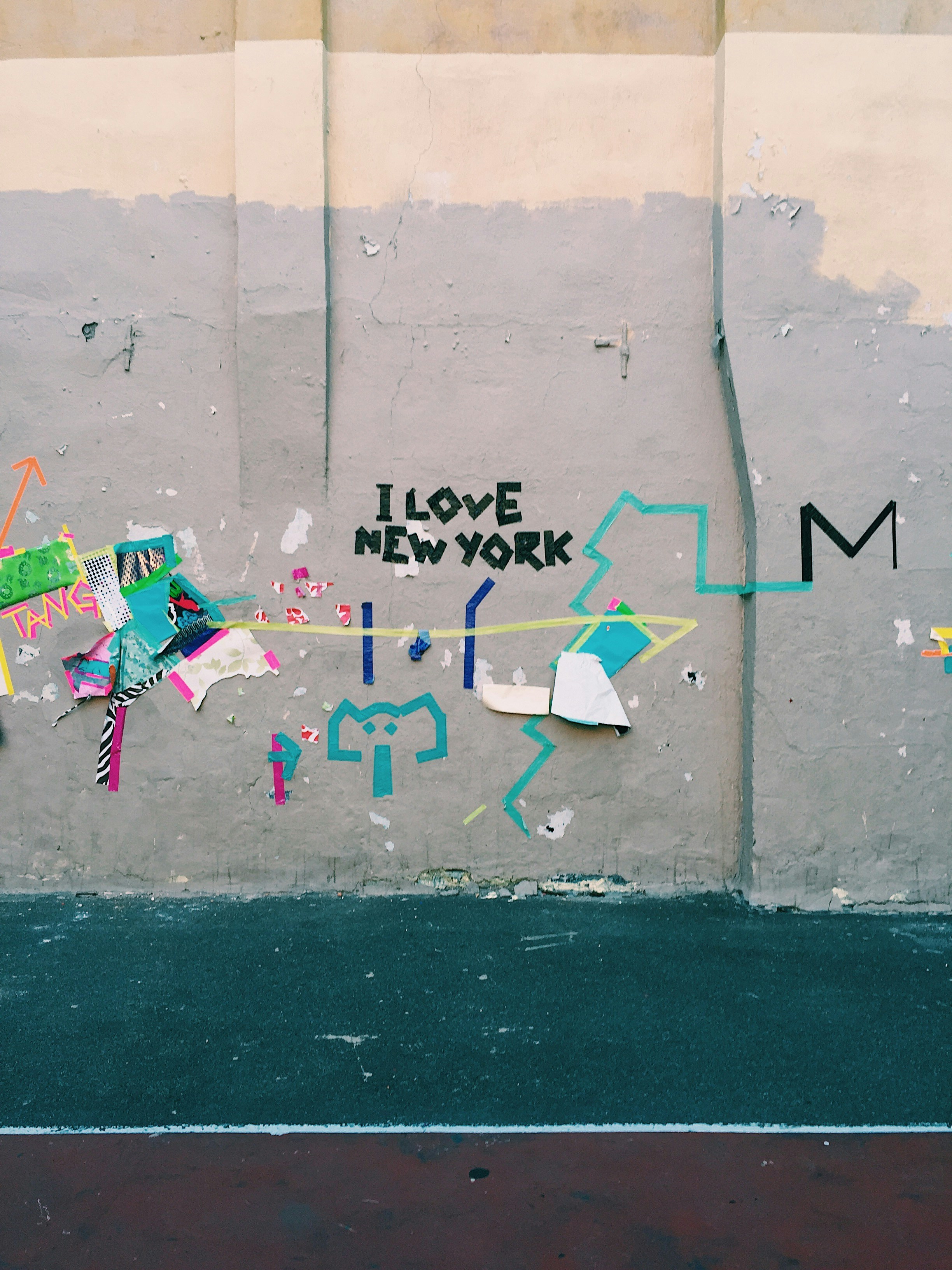 Colorful collage of paper and paint on a weathered wall, featuring the phrase 'I LOVE NEW YORK' amidst vibrant patterns and shapes.