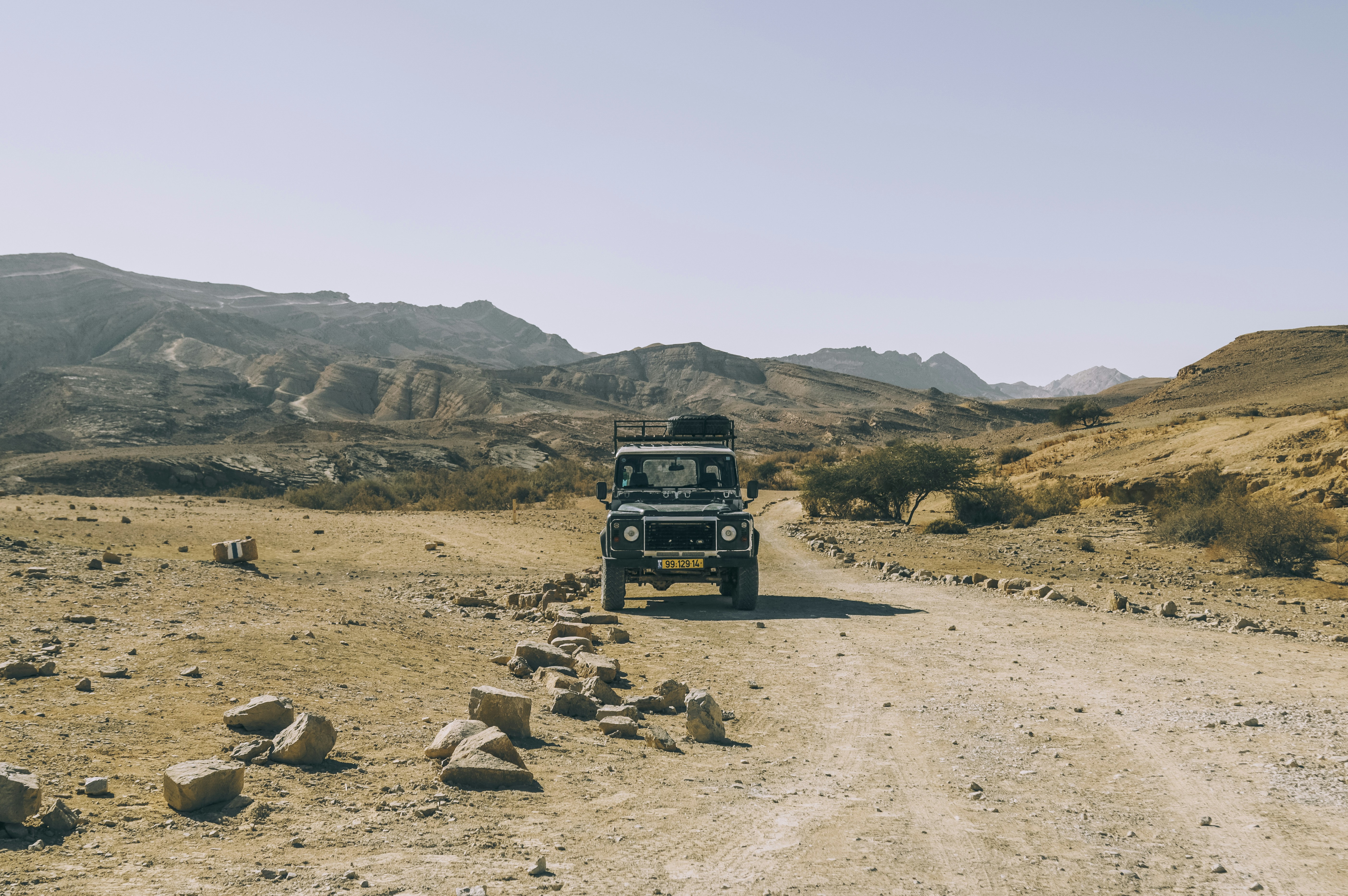Off-road vehicle navigating a rugged dirt path surrounded by barren hills and scattered rocks.