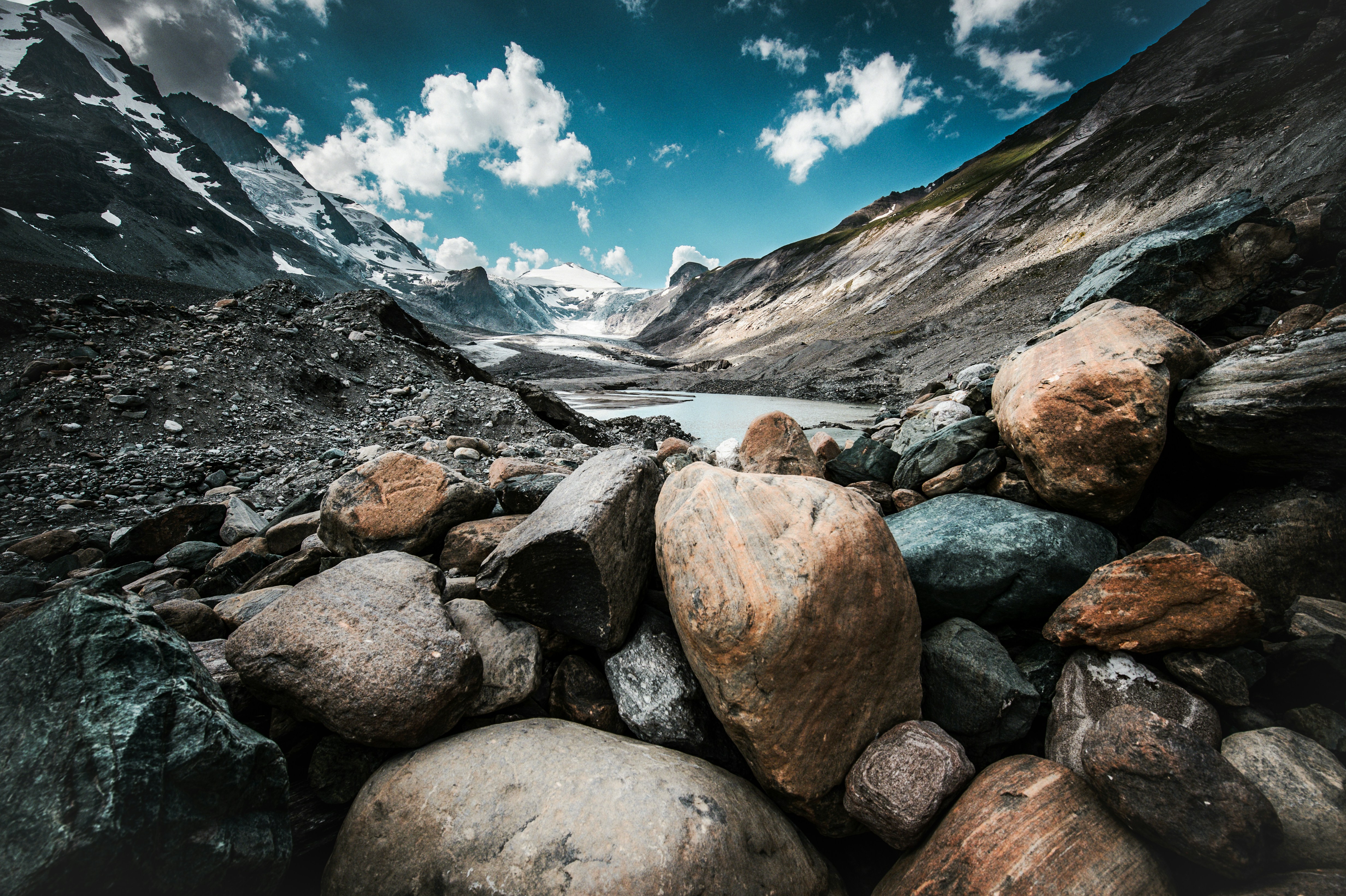 Foreground rocks lead to distant mountains under a vibrant blue sky with clouds.