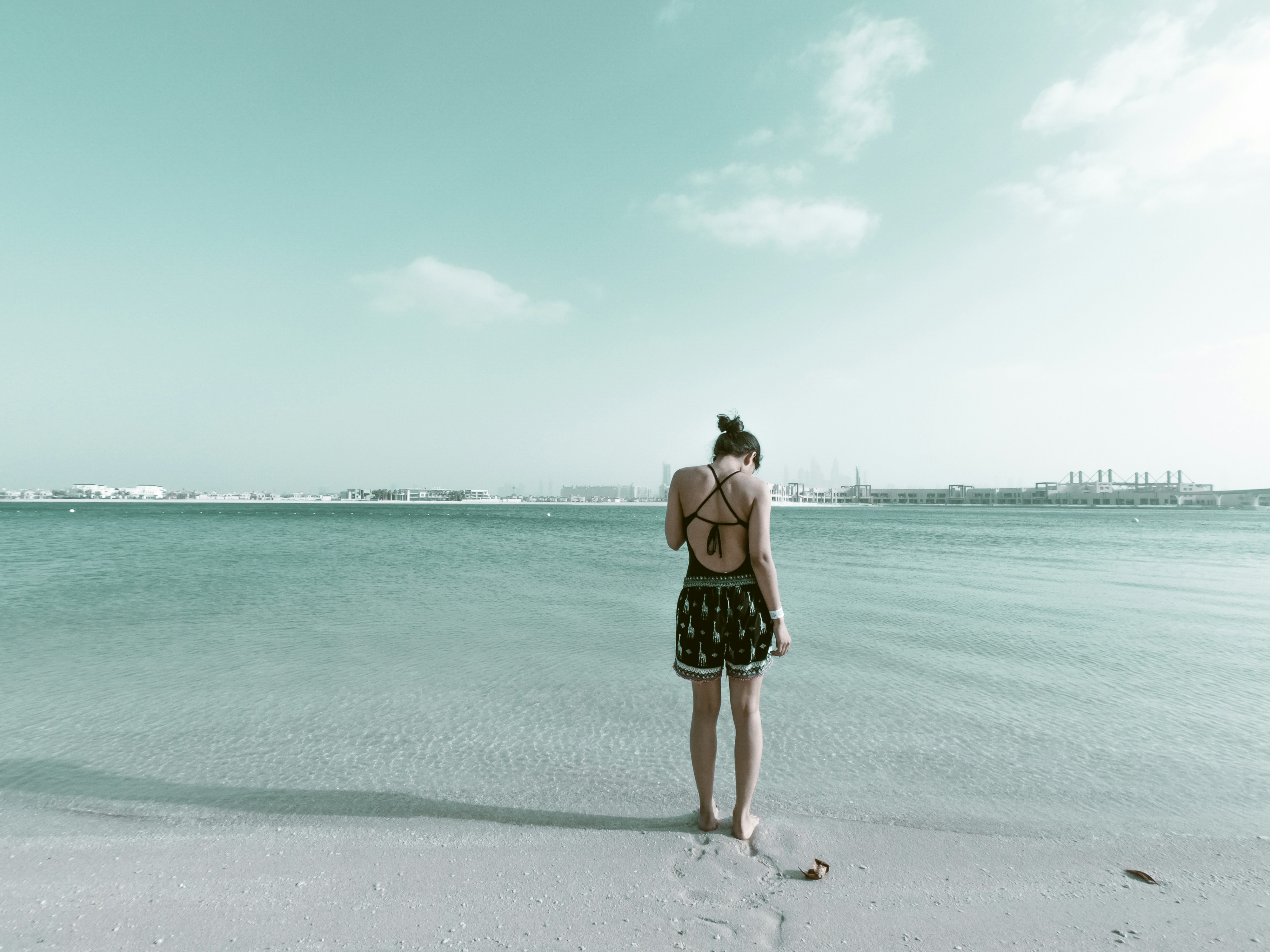 Person standing barefoot on the beach, gazing at the calm sea under a pastel sky. The scene evokes a sense of tranquility and reflection.
