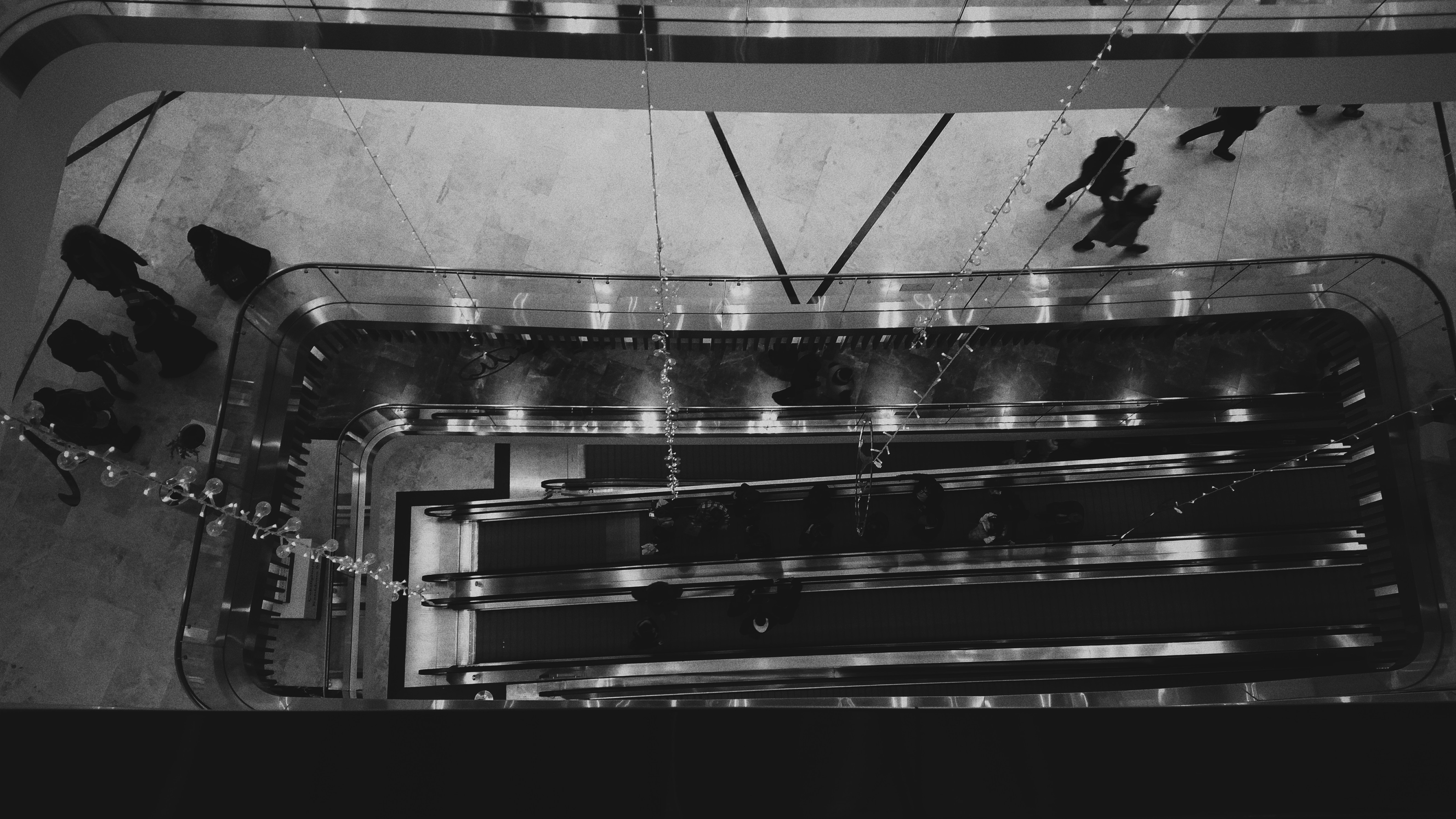Top-down view of a well-lit escalator in a shopping mall with people moving in various directions.