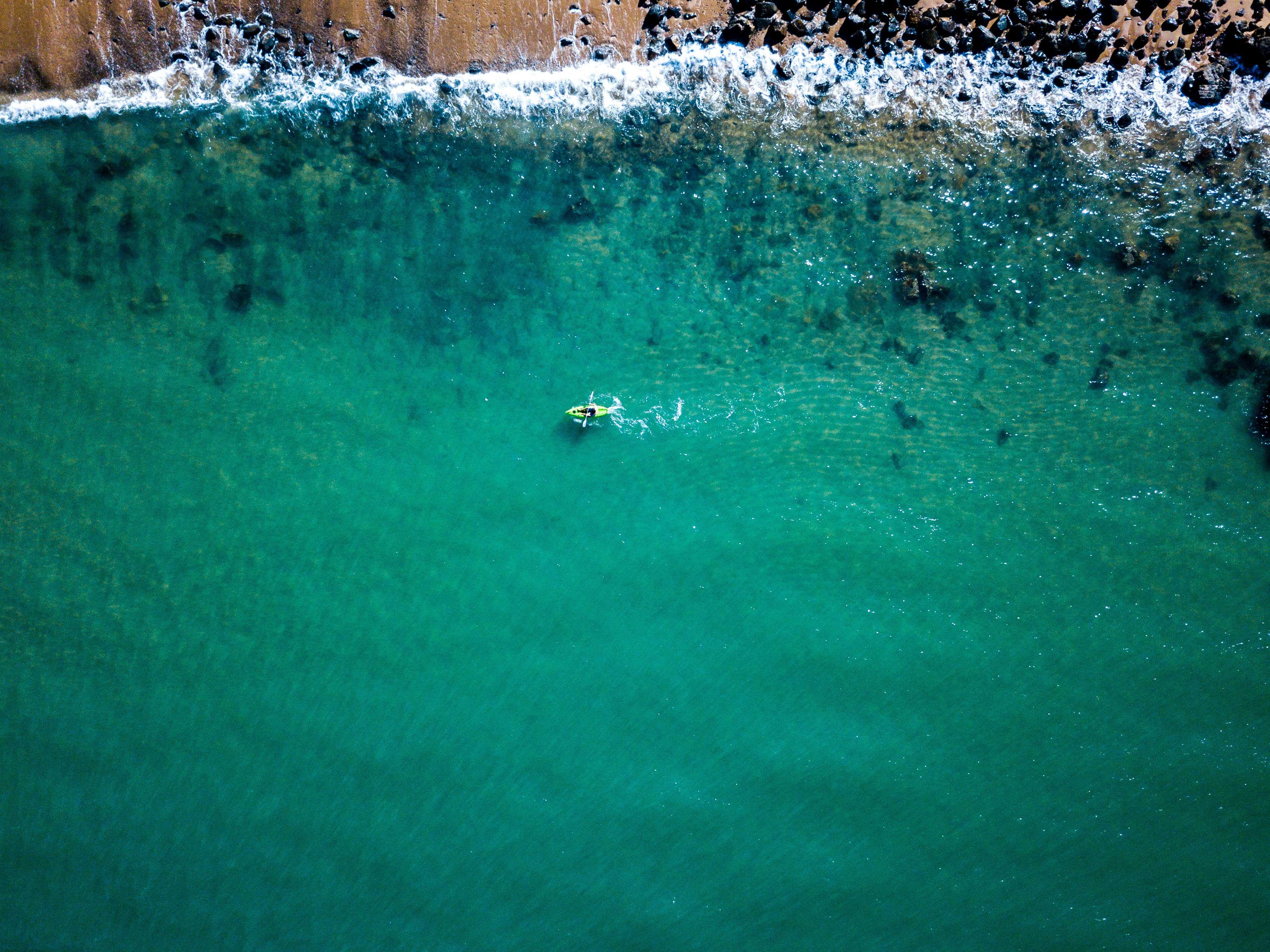 Kayaker paddling near rocky shoreline in clear turquoise sea.