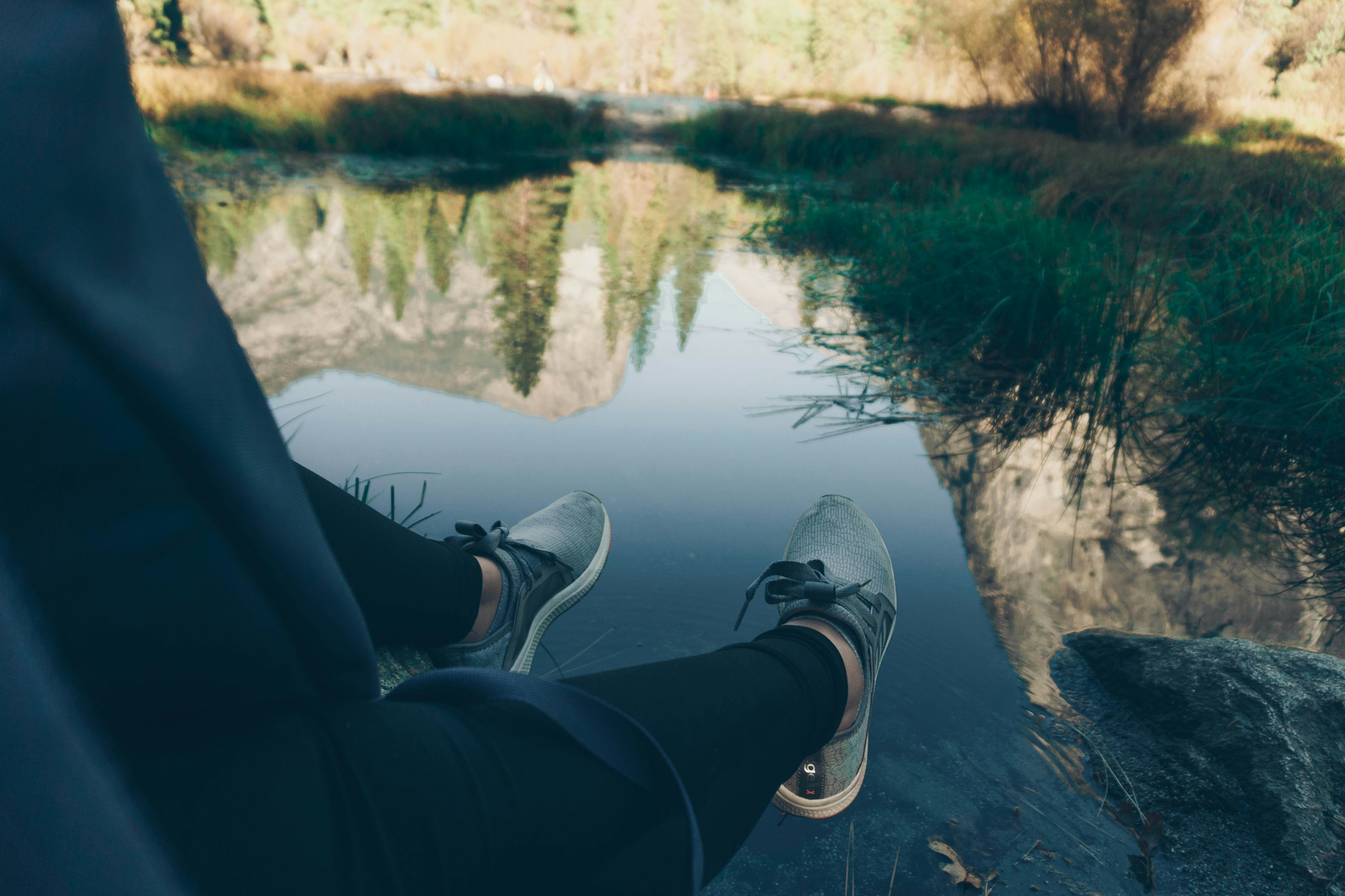 Shoes resting near a calm pond reflecting distant mountains and trees.