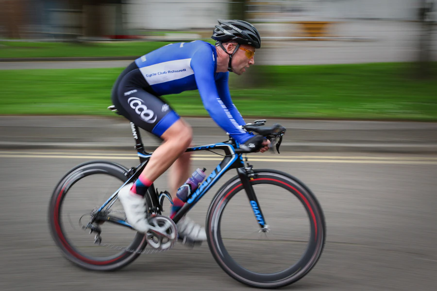 Cyclist in a blue skinsuit leaning forward on a racing bike, captured with motion-blurred background to convey speed.