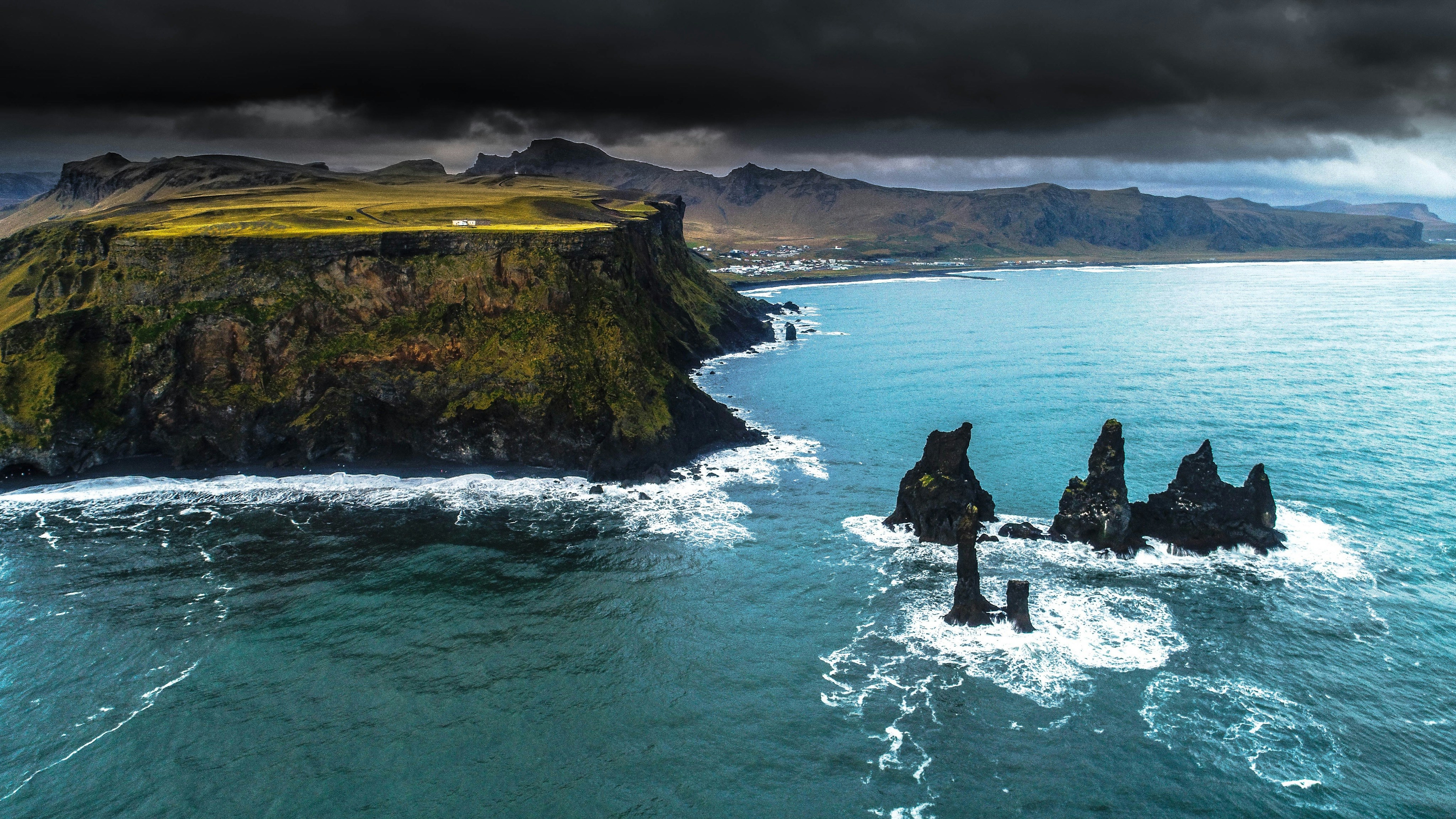 Reynisdrangar | black sea stacks surrounded by body of water beside mountain under cloudy sky