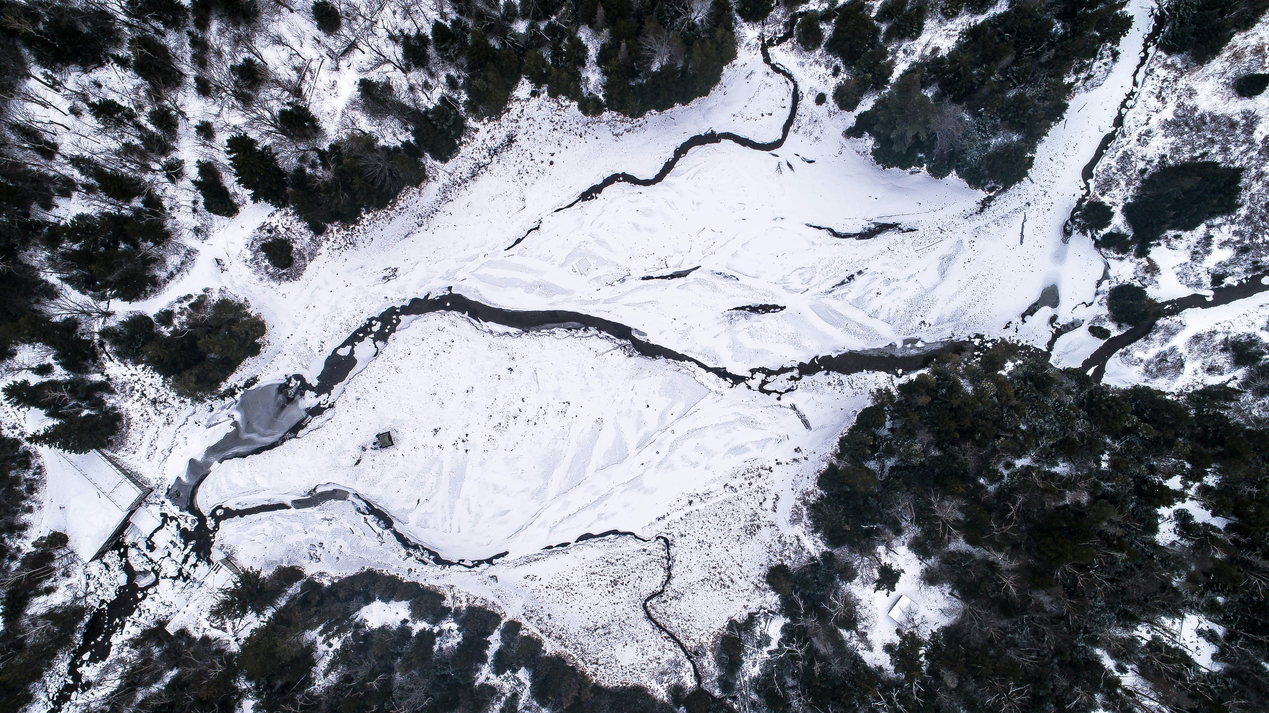 Snow-covered landscape with winding dark river and surrounding trees.