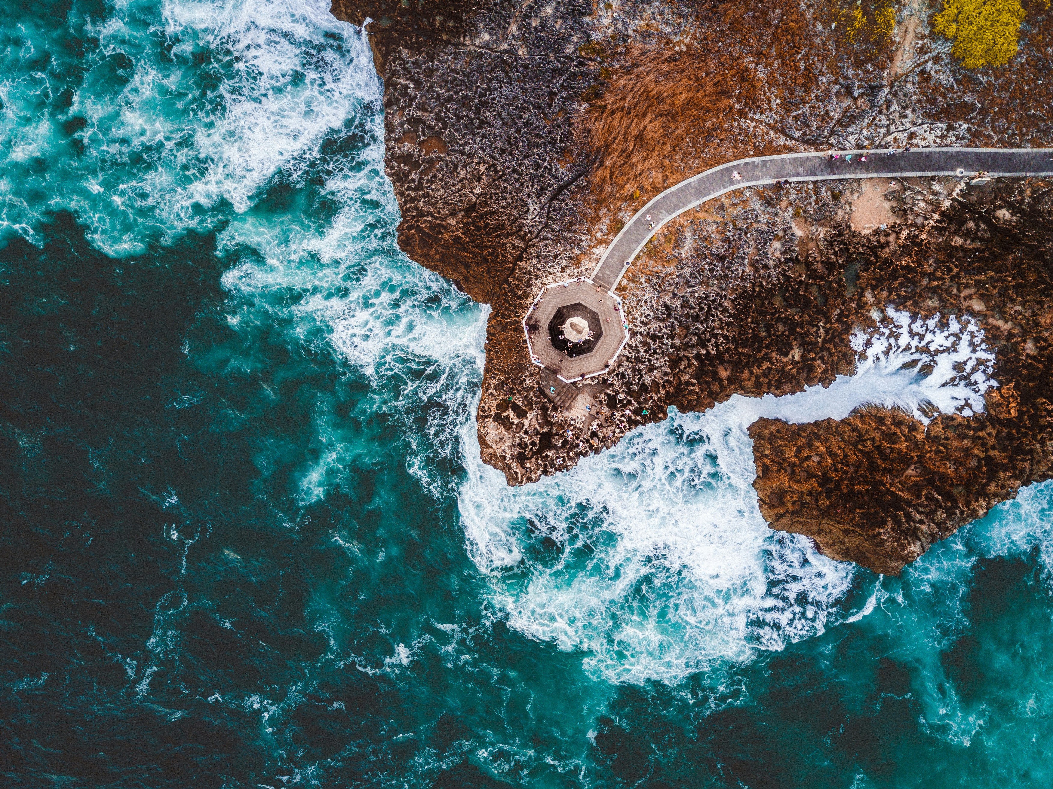 Aerial view of a coastal lookout point surrounded by crashing waves, showcasing the rugged shoreline and vibrant turquoise waters.