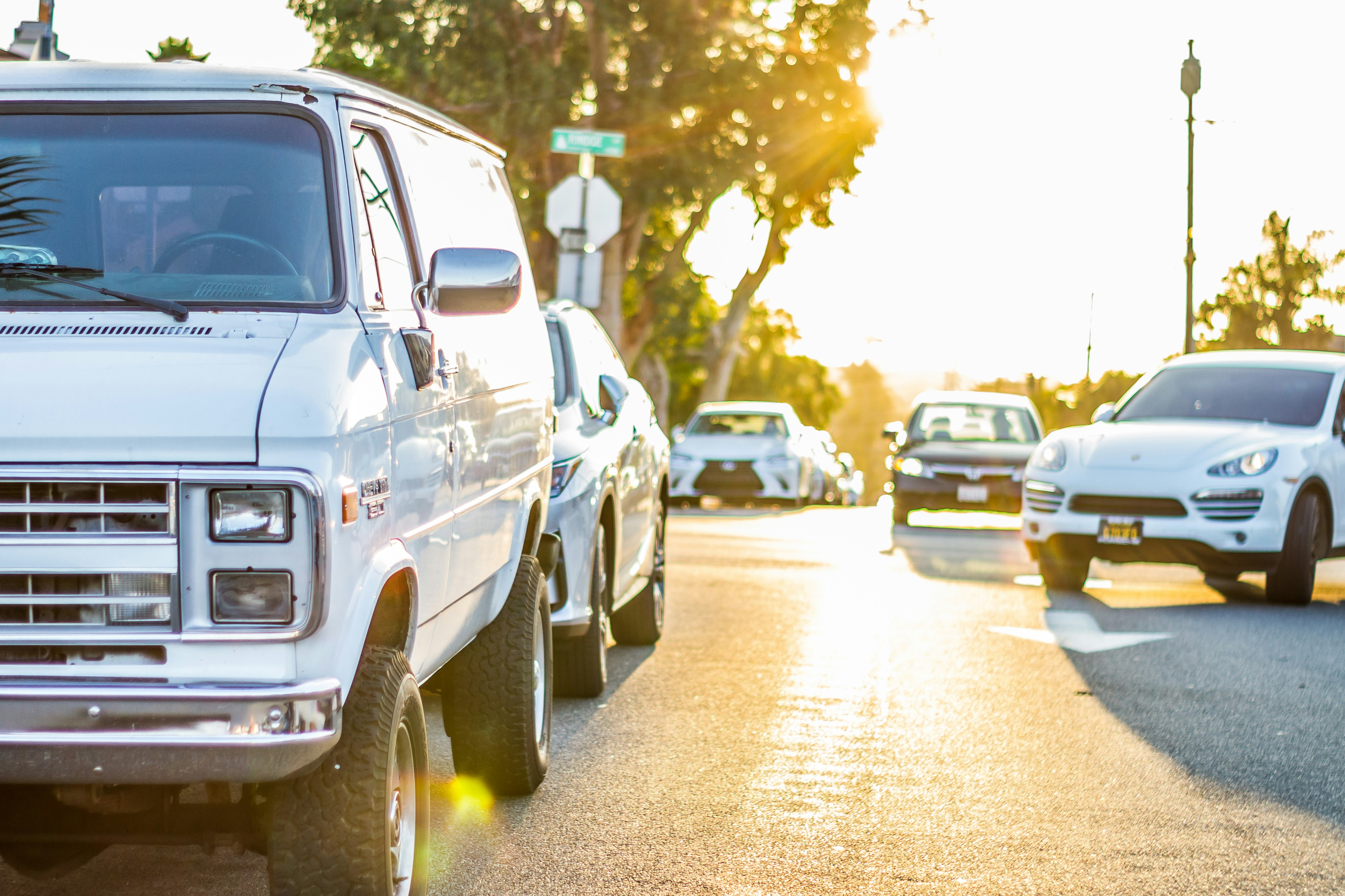 White van parked on a sunlit street with cars in motion blurring in the background.