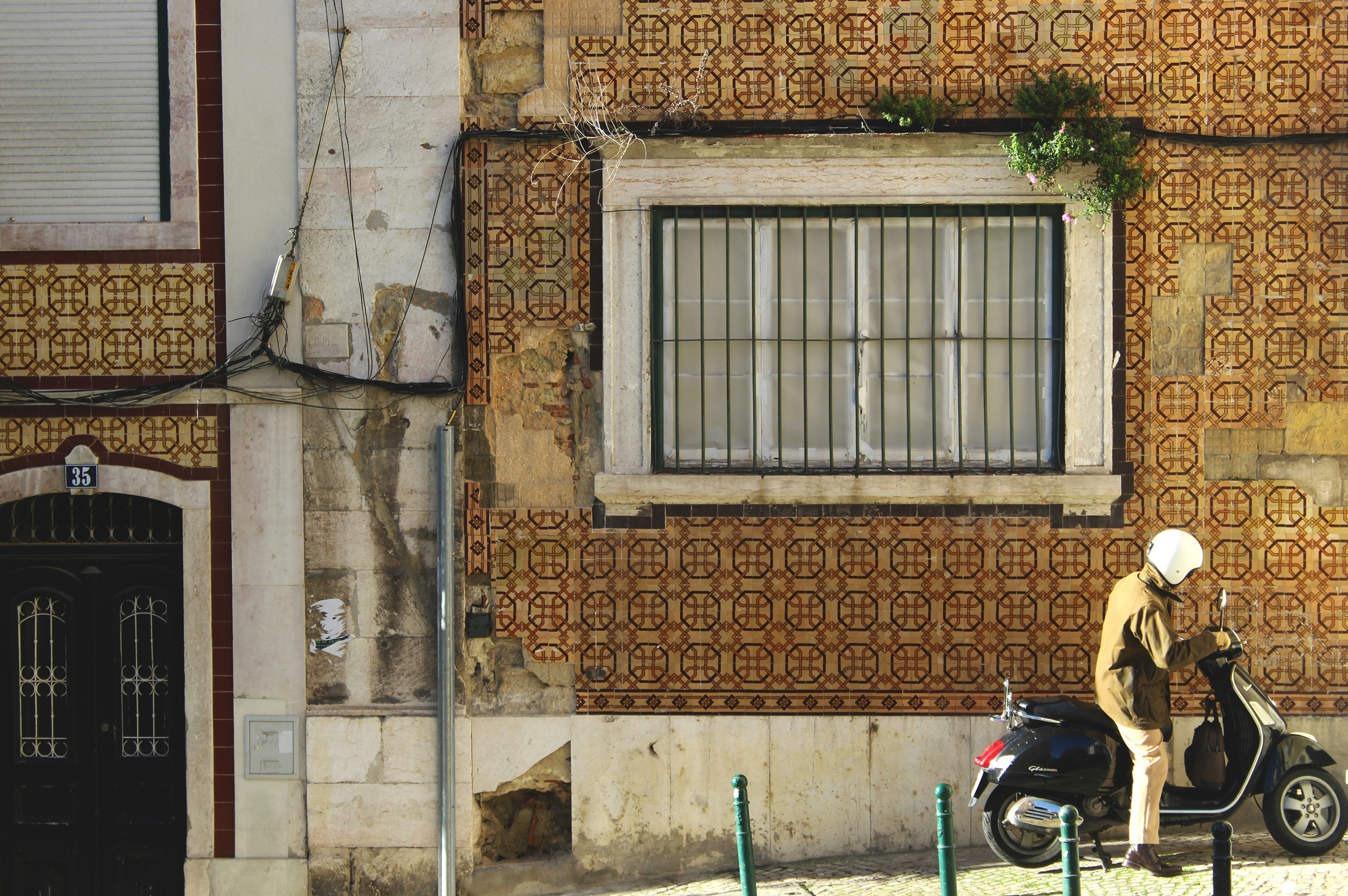 Person on a motorcycle beside a patterned tiled building in bright daylight.