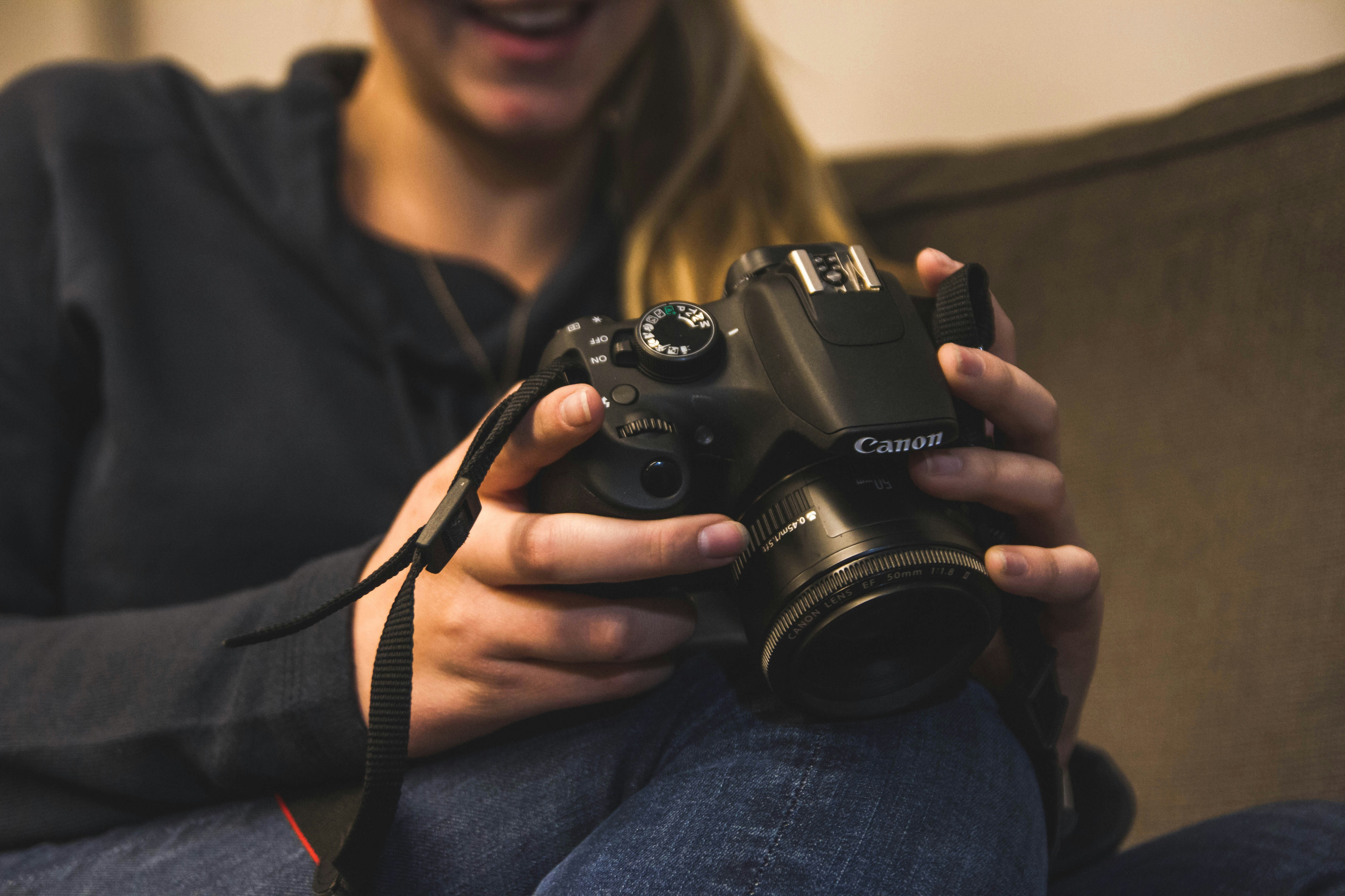 A person holds a Canon EOS 7D camera, focused on the intricate details of the device while seated comfortably. The scene captures the essence of photography as a creative pursuit.