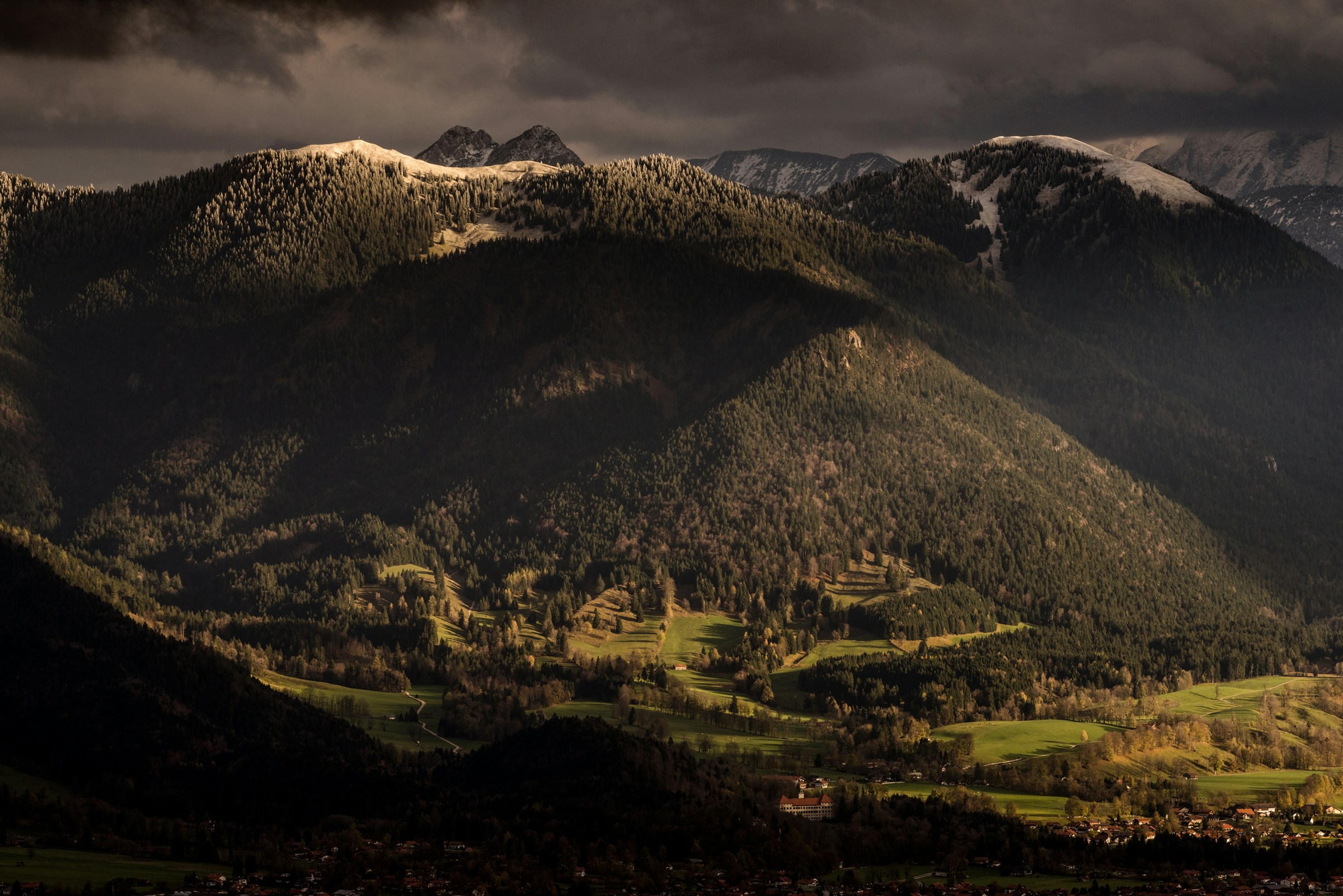 Sunlight breaks through clouds, illuminating green valleys and snow-capped mountains.