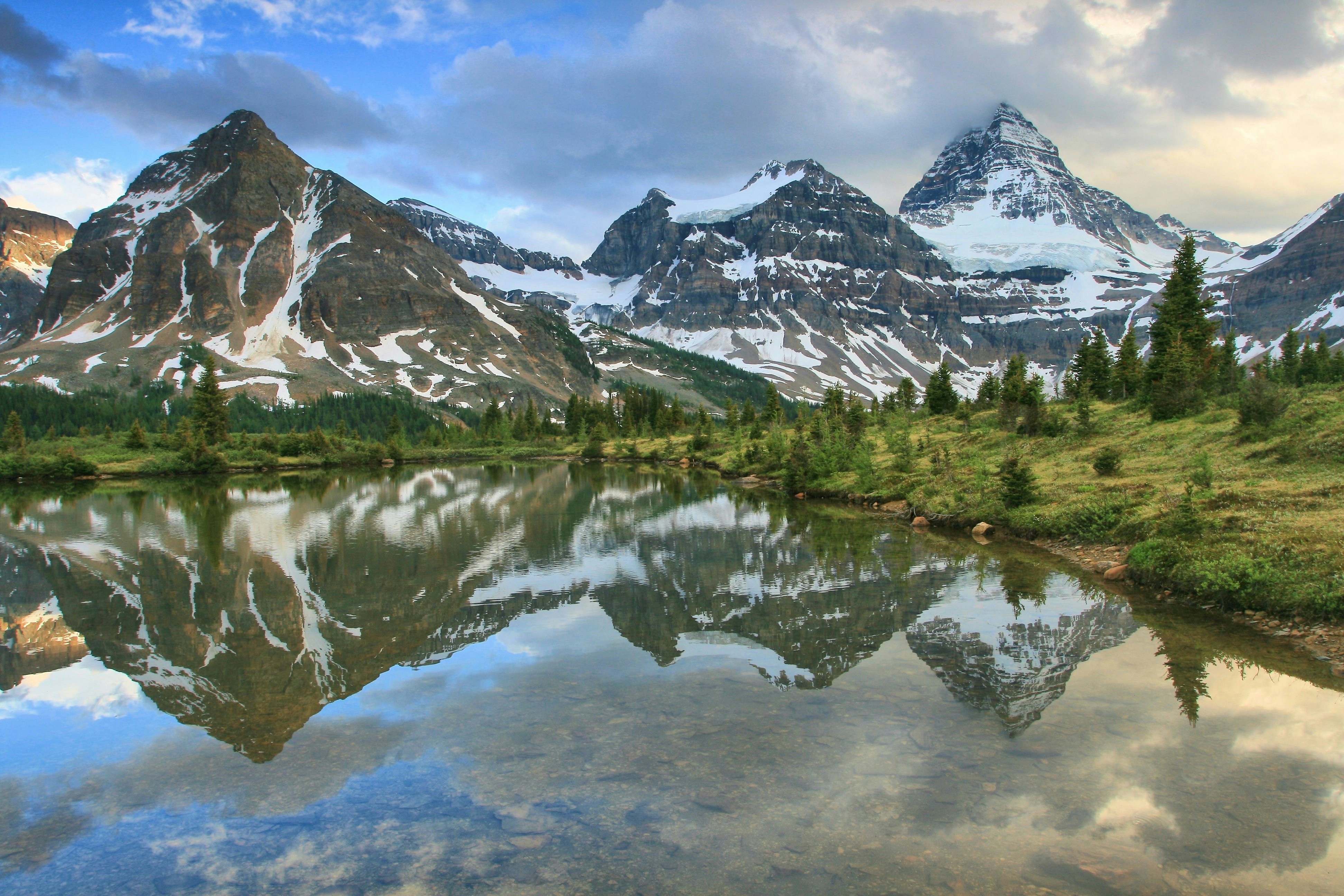 Serene lake reflecting rugged glacier-covered mountains under a vibrant sky.