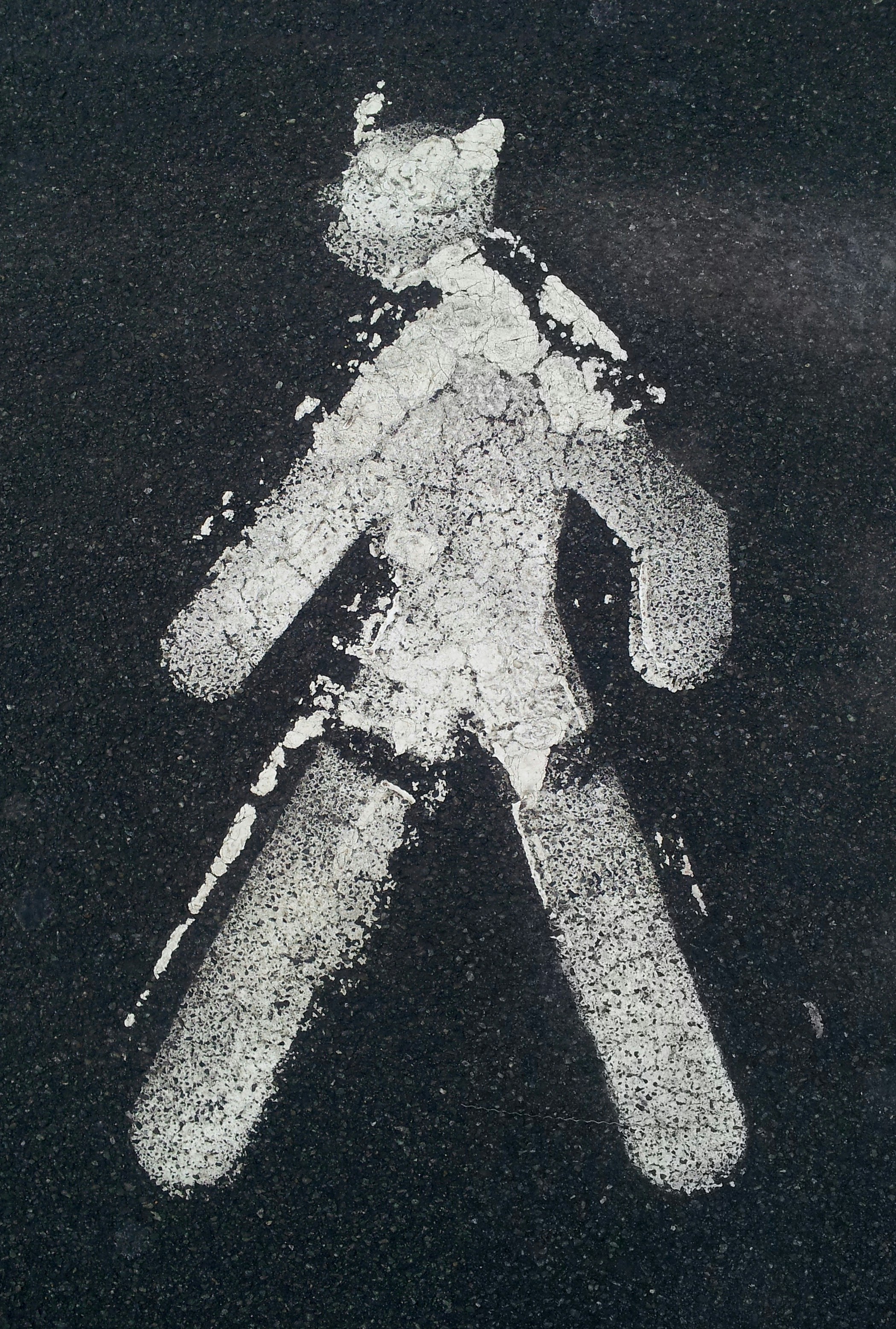 Worn pedestrian symbol on asphalt, showcasing the effects of weathering and wear over time.