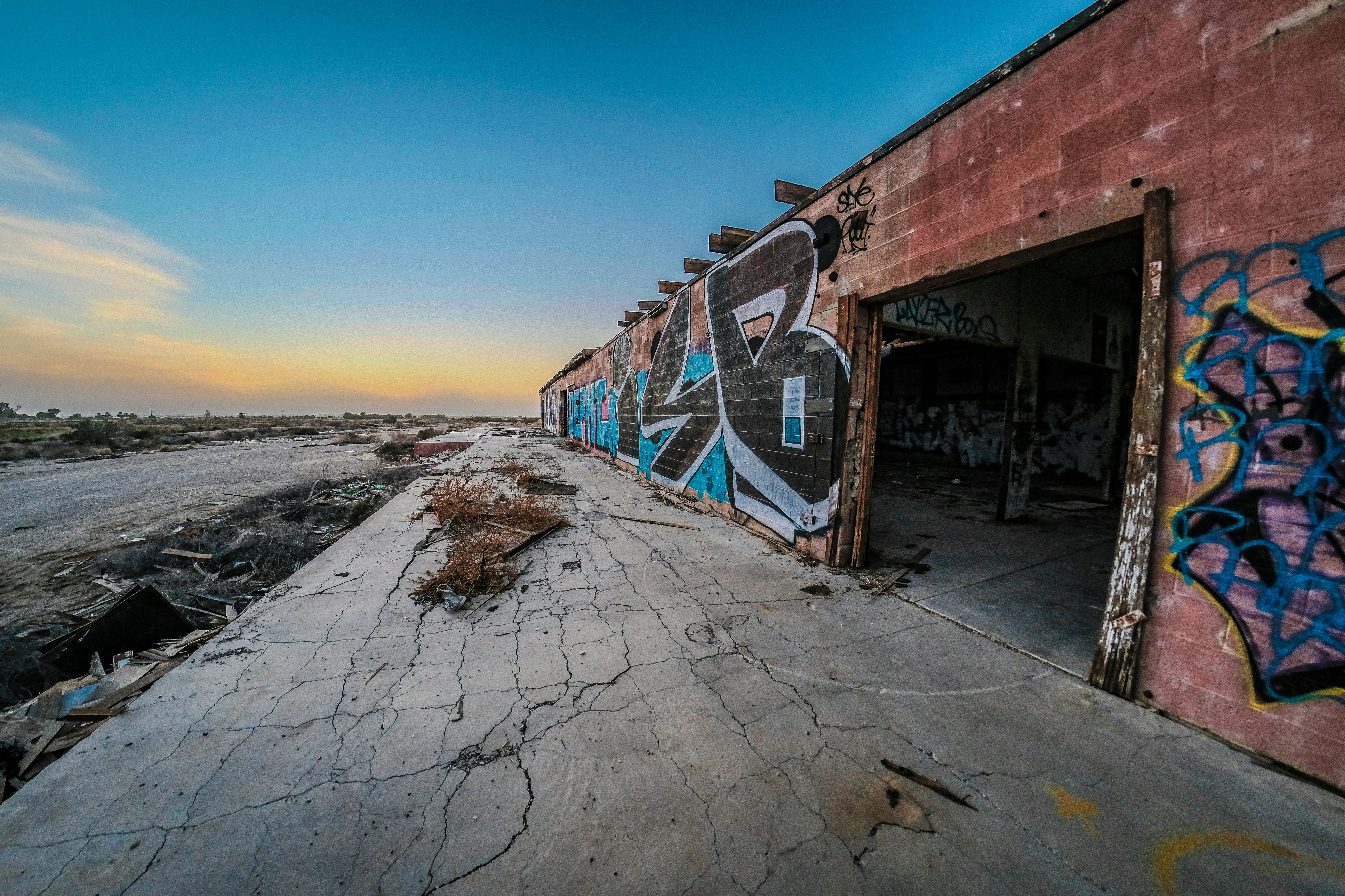 Graffiti-covered abandoned building against a sunset sky in a desolate landscape.