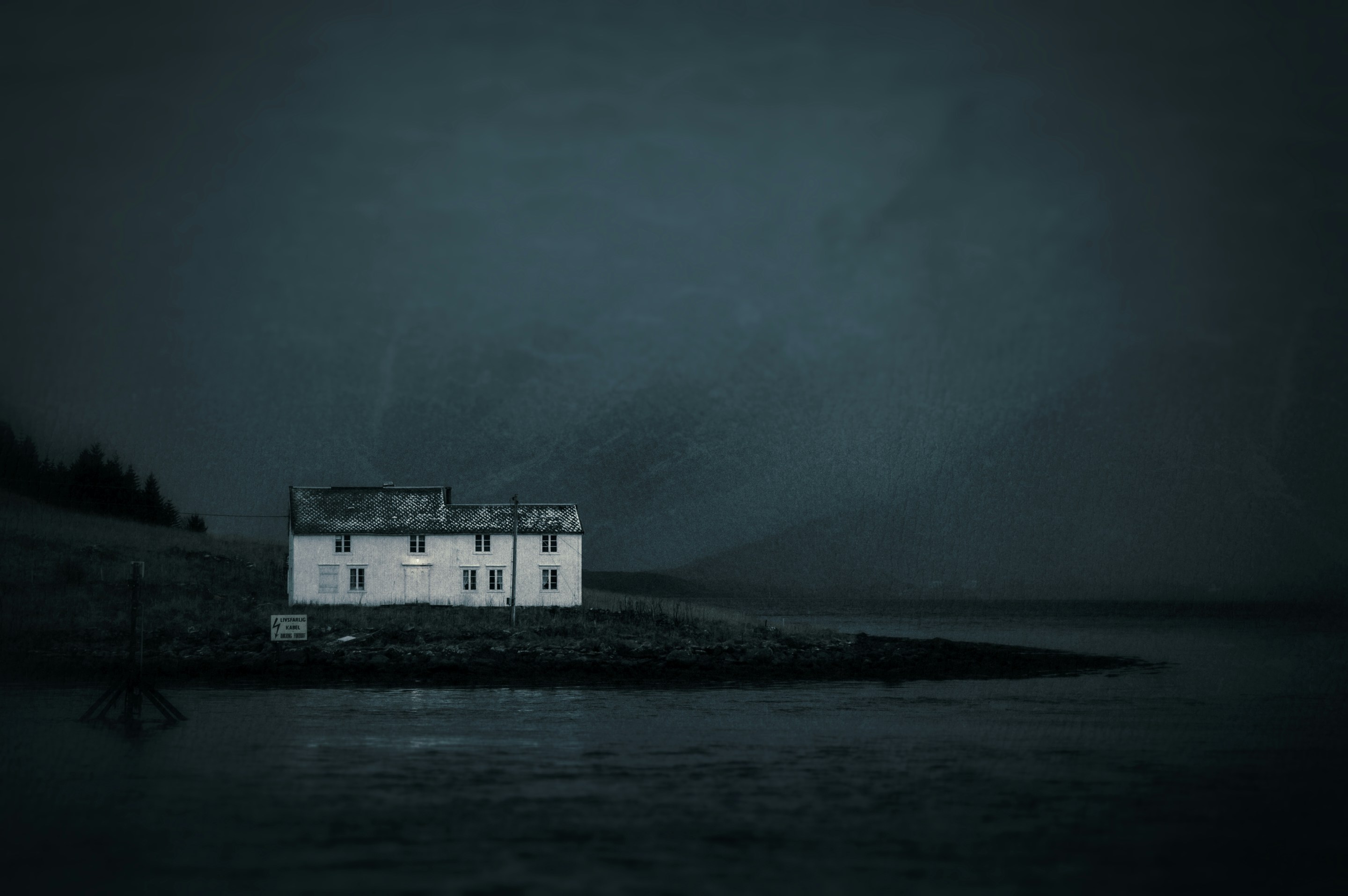 Lonely white house standing against a dark, moody seascape, surrounded by a misty atmosphere.