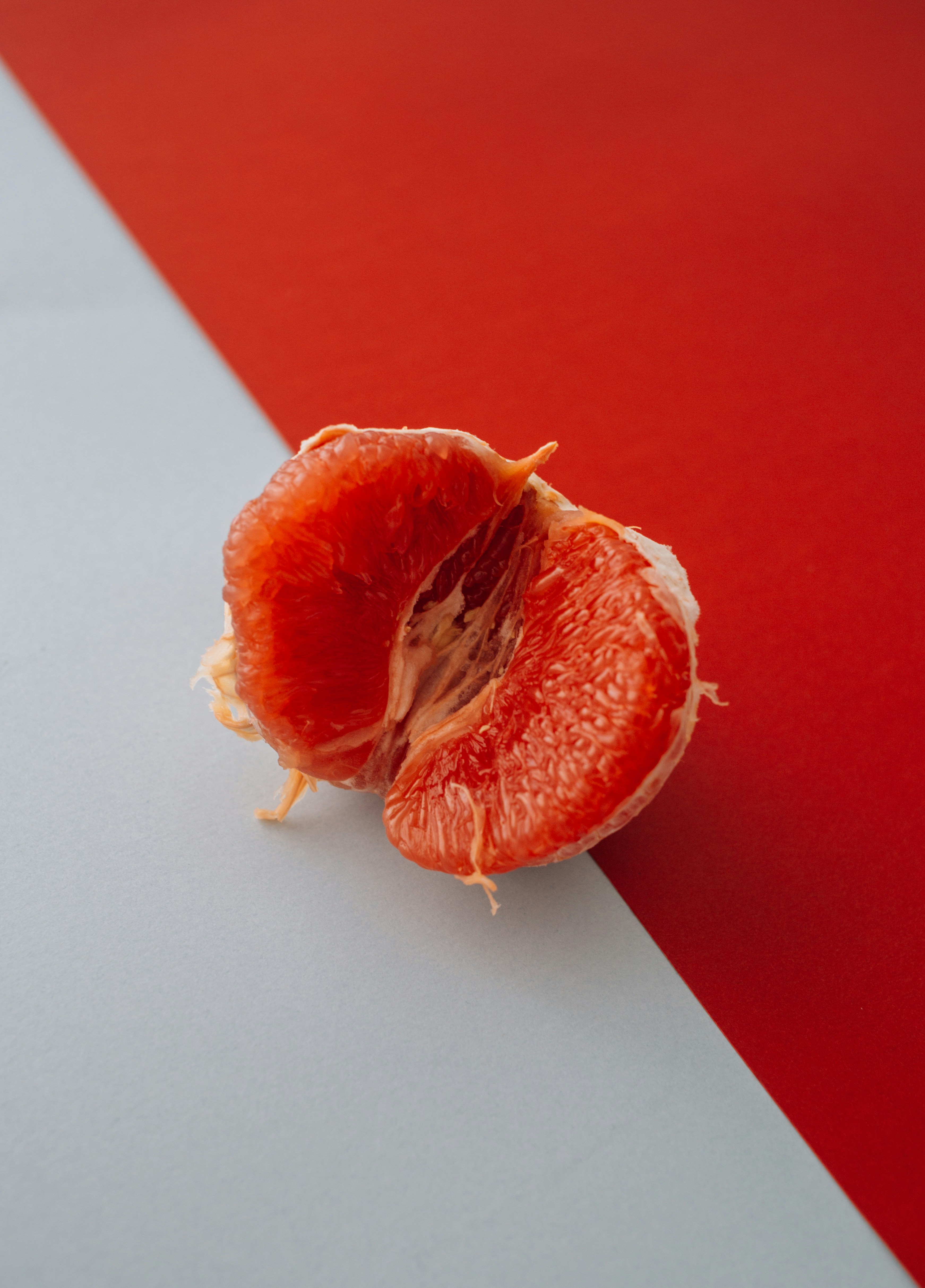 A vibrant slice of citrus fruit rests on a bold geometric background of red and gray, highlighting its juicy texture and vivid color.
