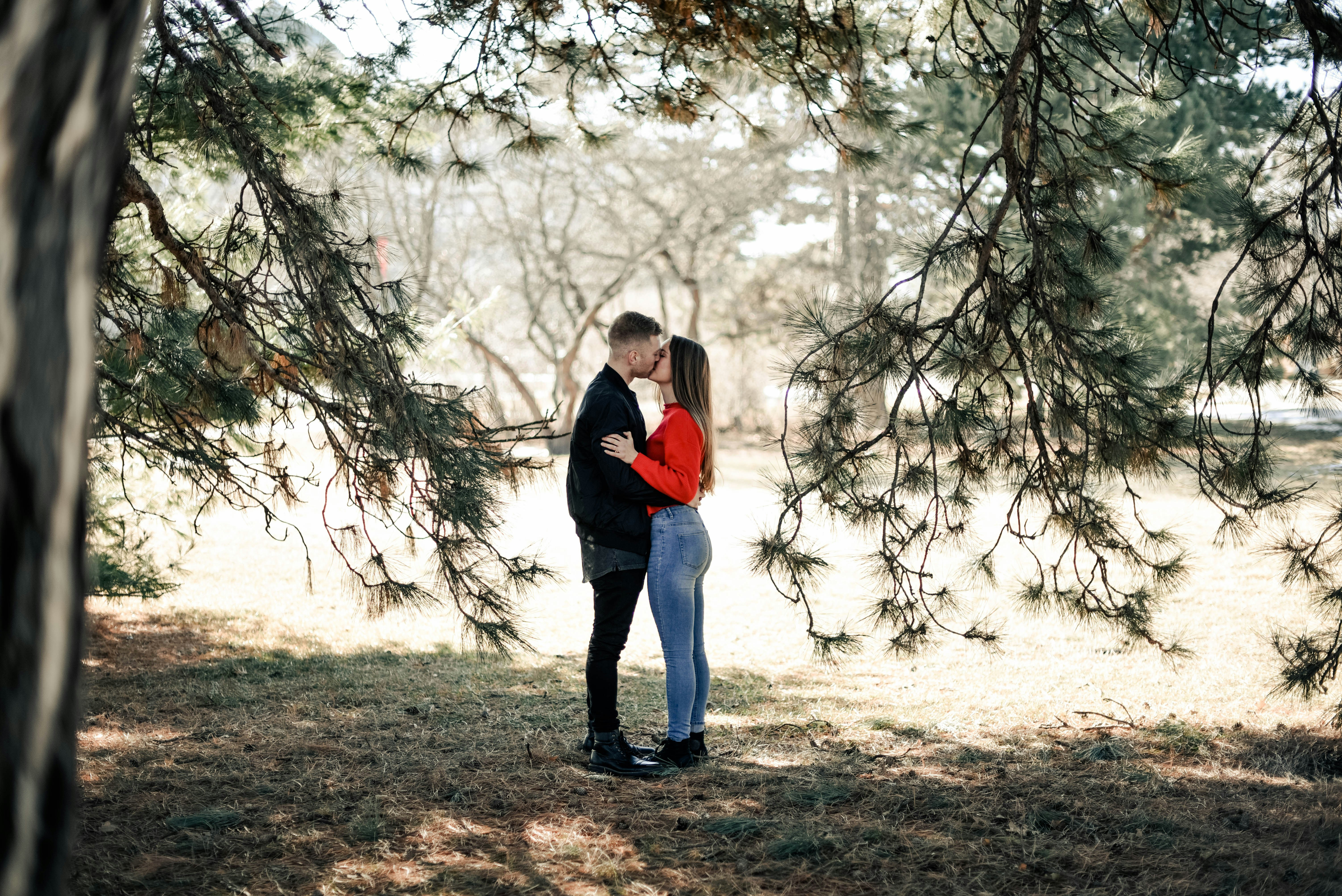 Couple embracing under a sun-dappled tree in a park.