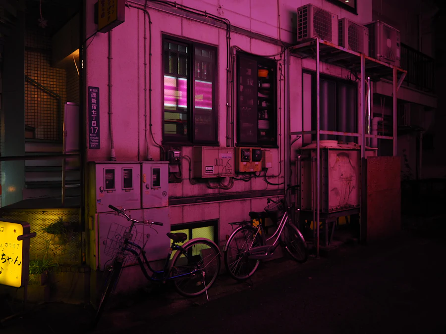 Two bicycles parked beside a building illuminated by vibrant pink and purple neon lights.