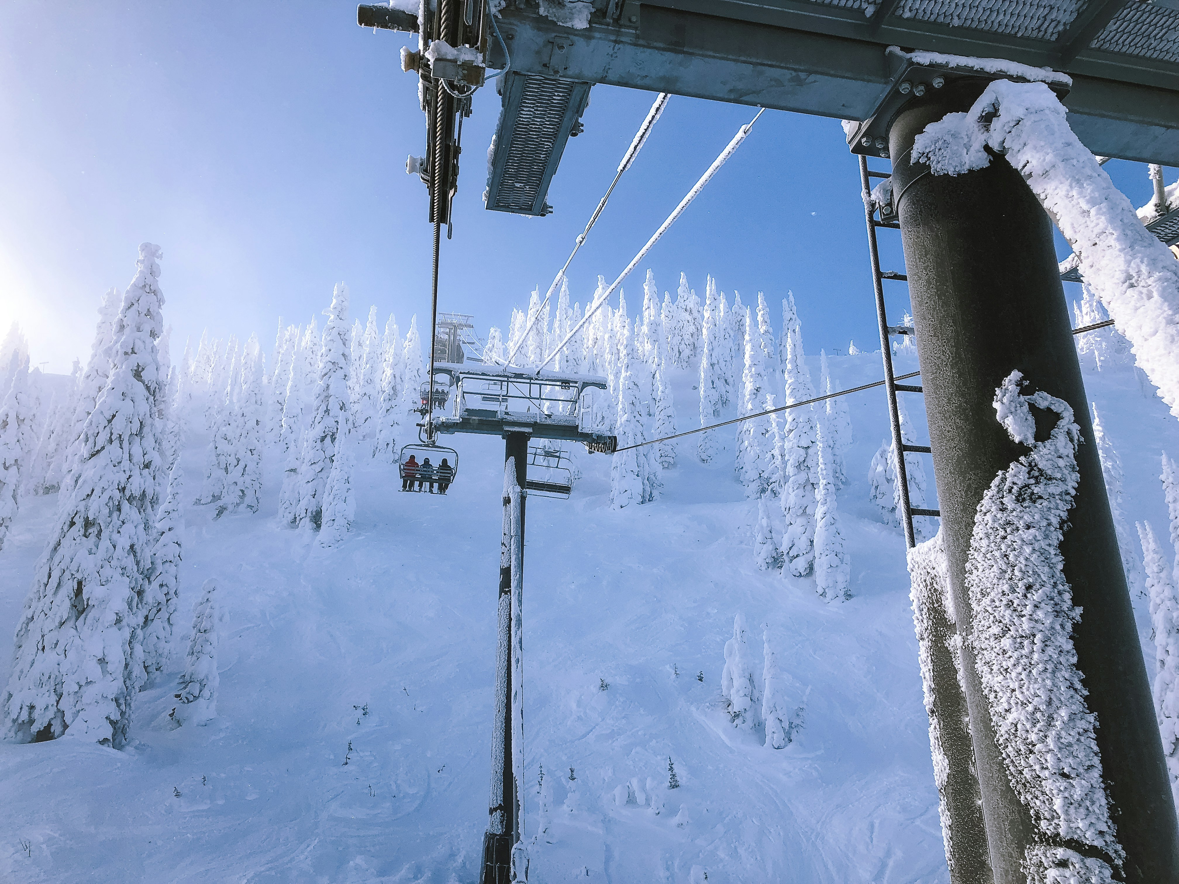 white and black cable transportation with three person riding near trees covered of snow at daytime
