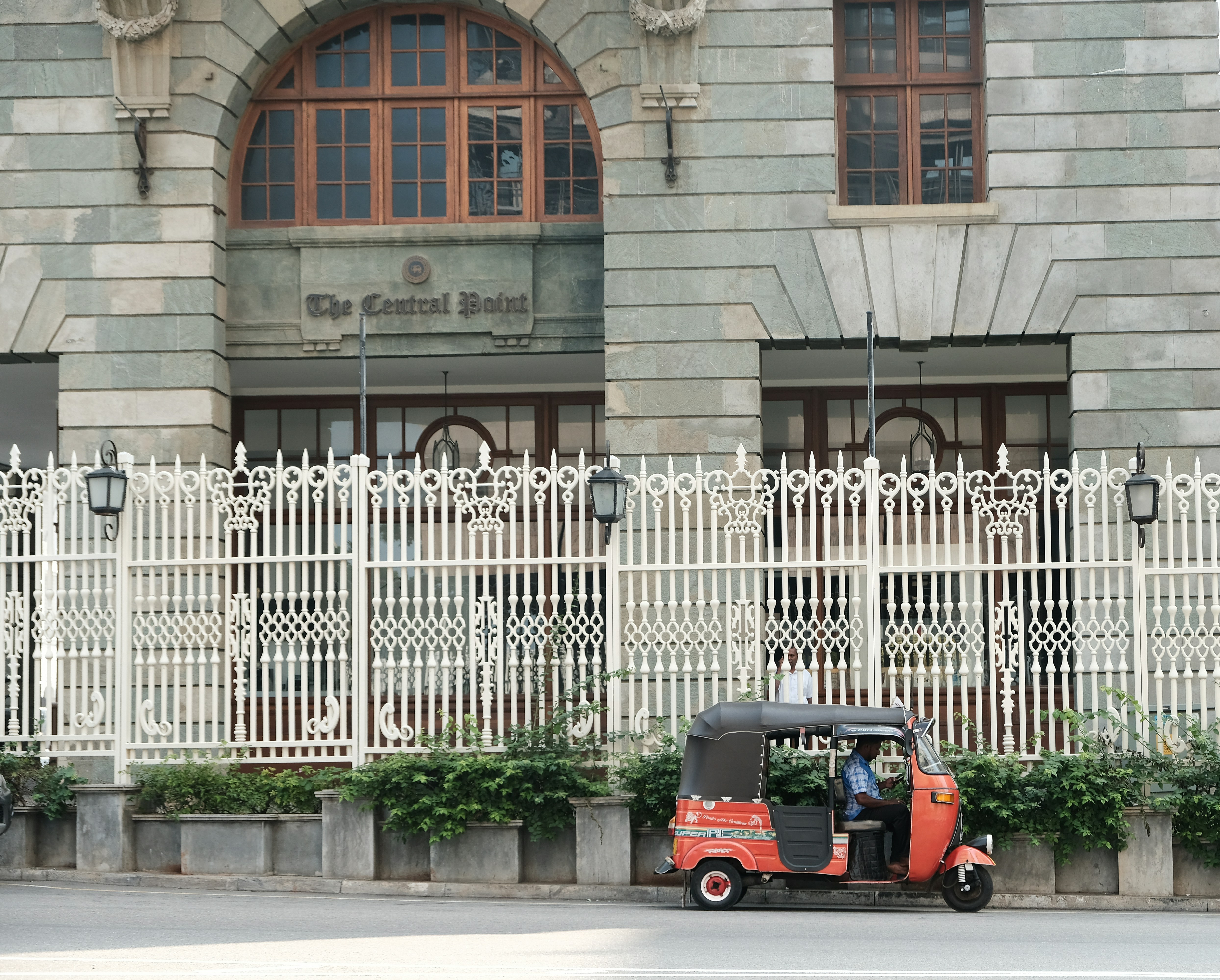 Red rickshaw parked in front of an ornate, historic building with white wrought iron fence.