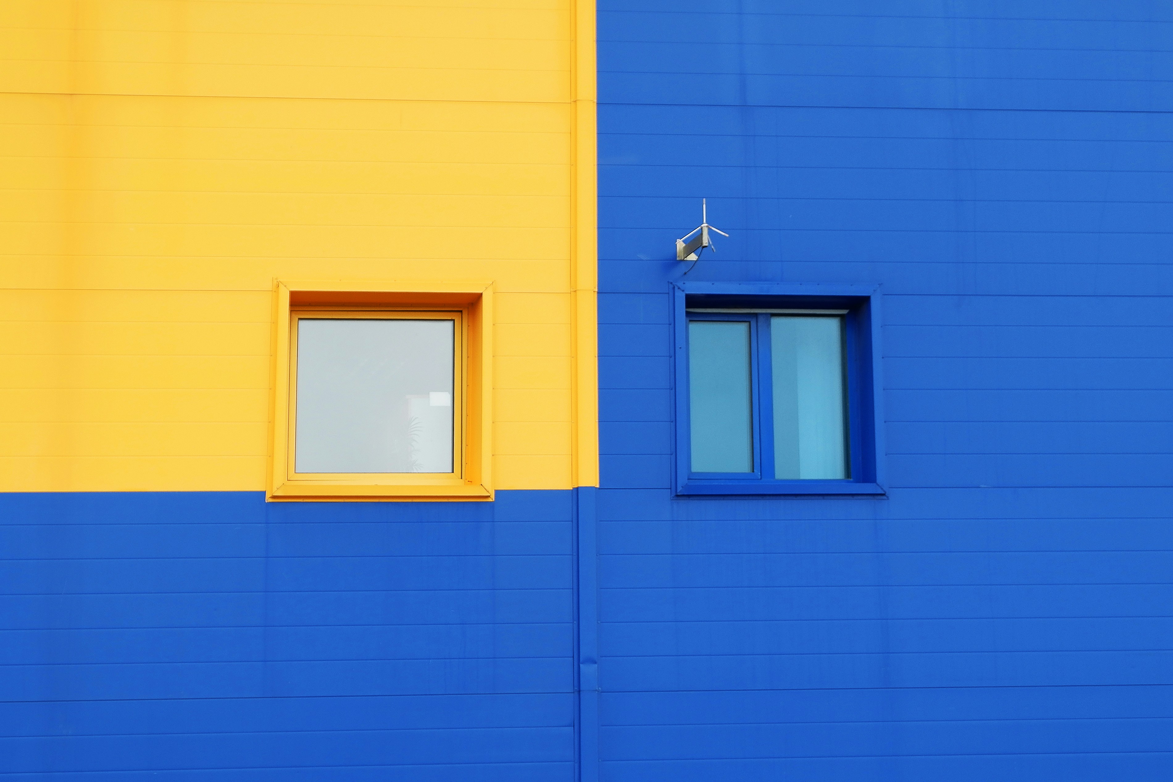 Bright yellow and deep blue facade with two windows and a security camera creating a striking color contrast.