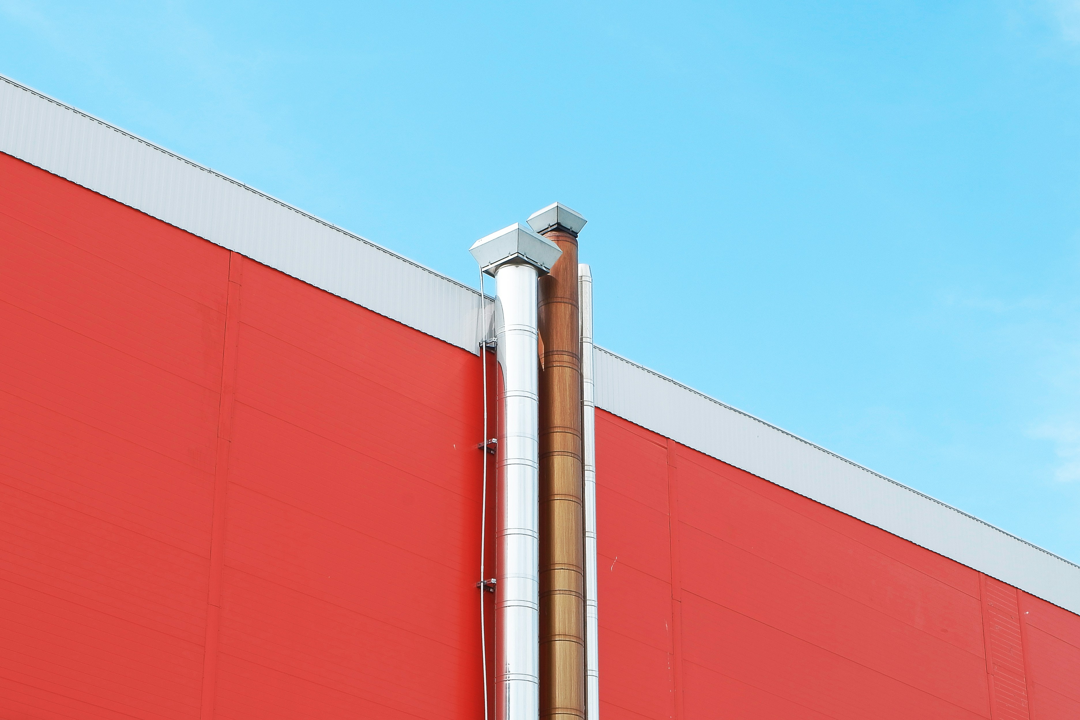 Red wall with a silver drainpipe under a bright blue sky.