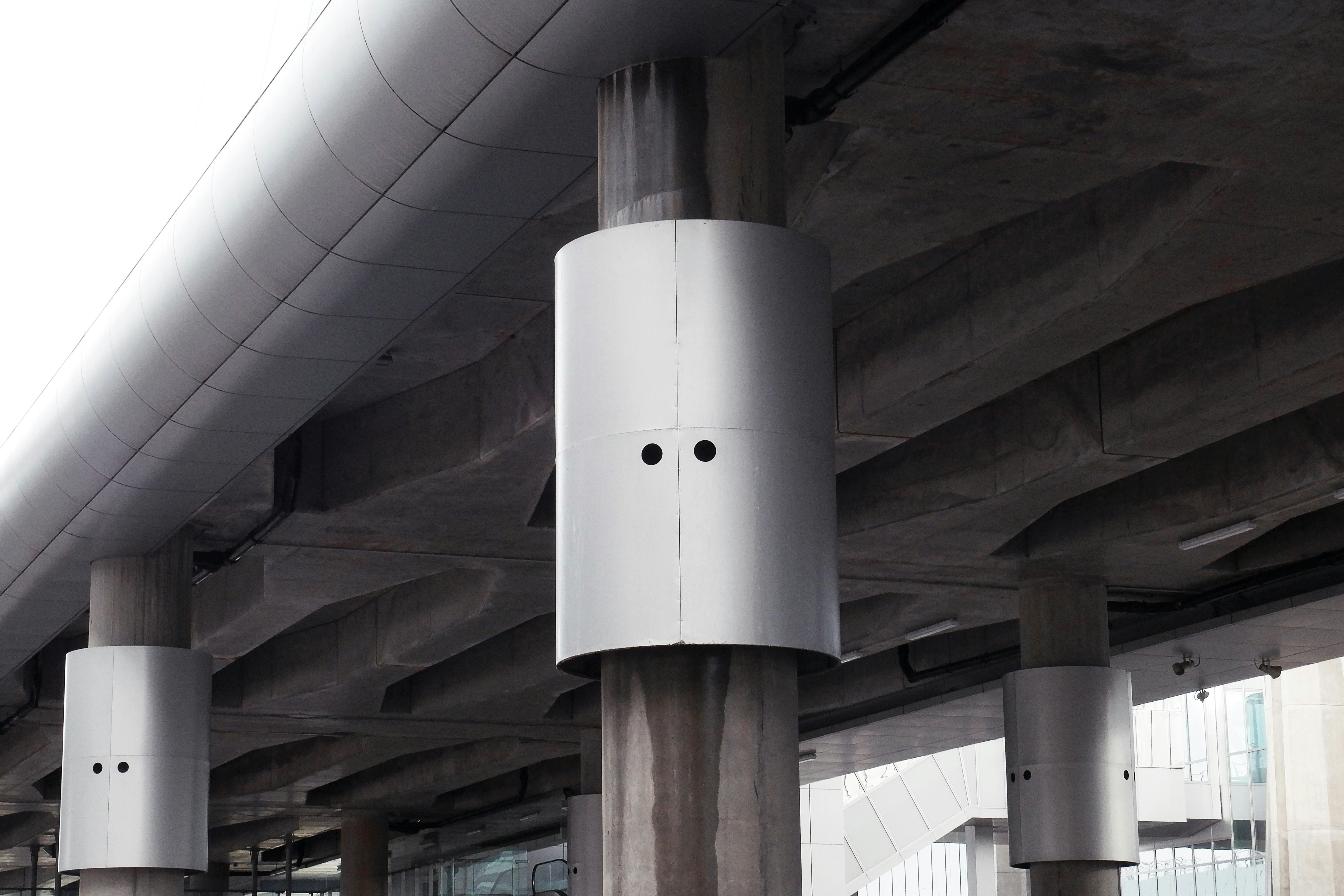 Concrete pillars with metallic covers resembling faces under an overpass.