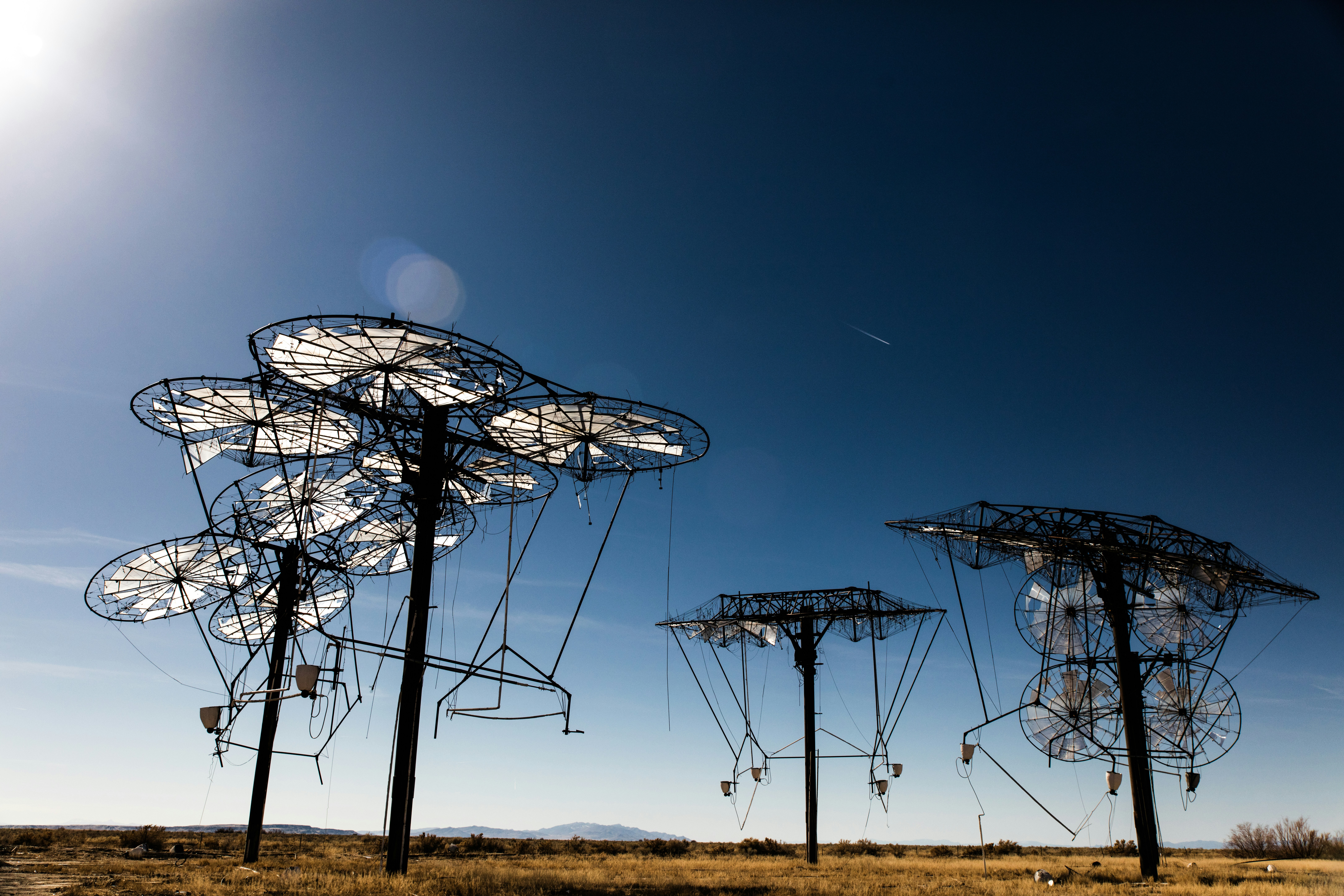 Array of solar panel structures silhouetted against a deep blue sky in a rural landscape.