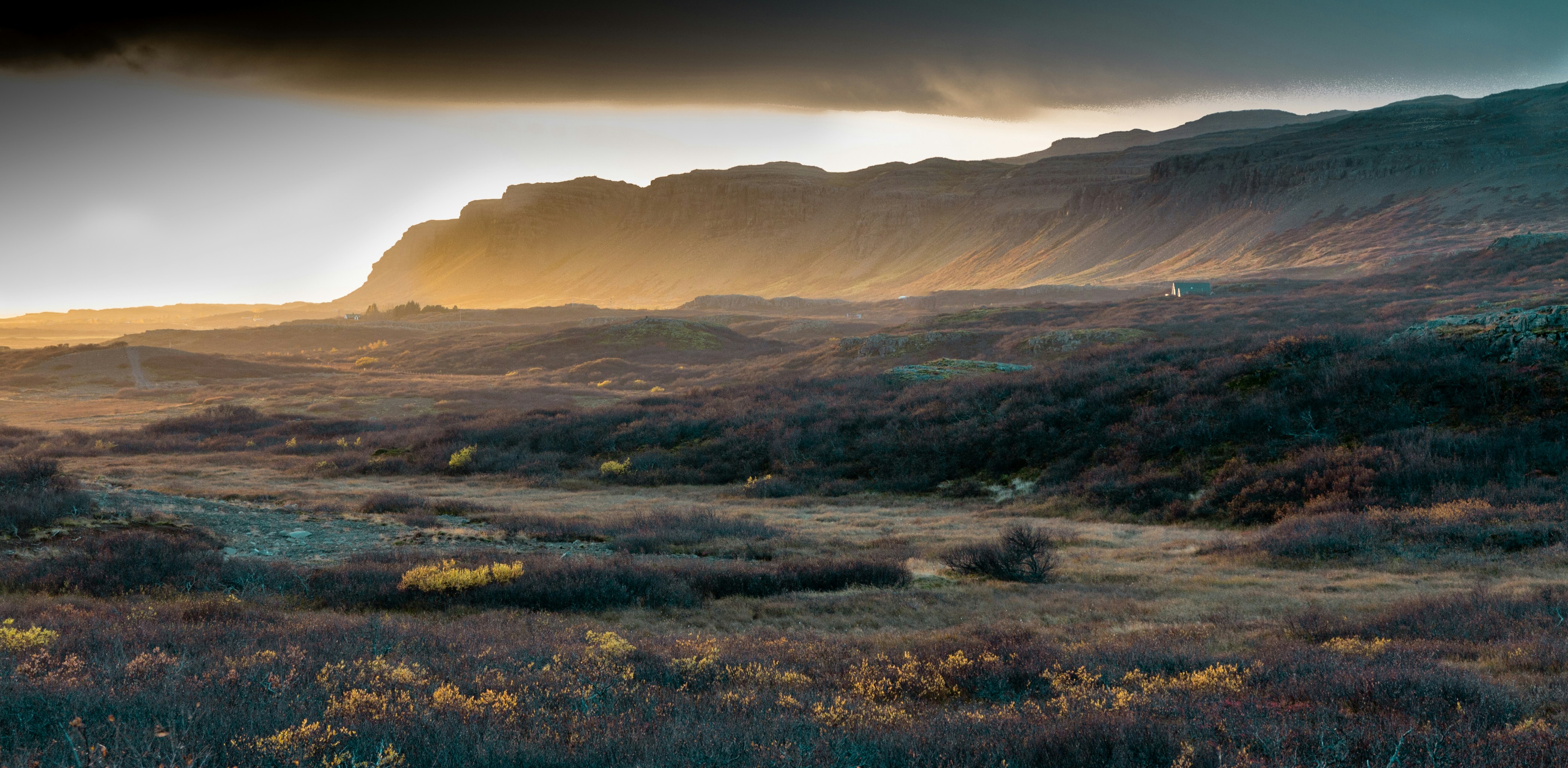 Sunset casts a warm glow over cliffs and a vast plateau under overcast skies.