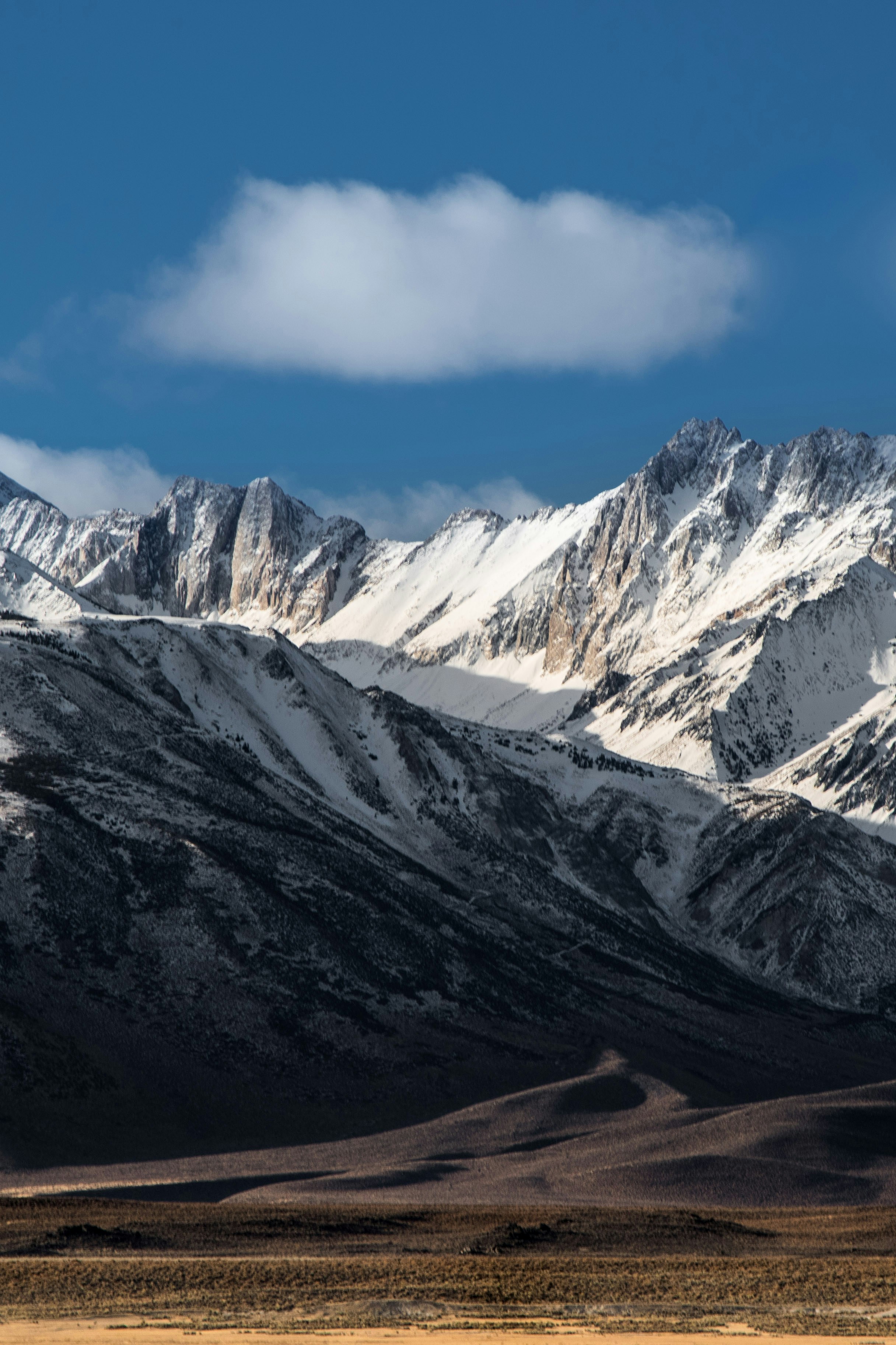 Snow-capped mountain range under a clear blue sky, showcasing rugged terrain and dramatic cliffs.