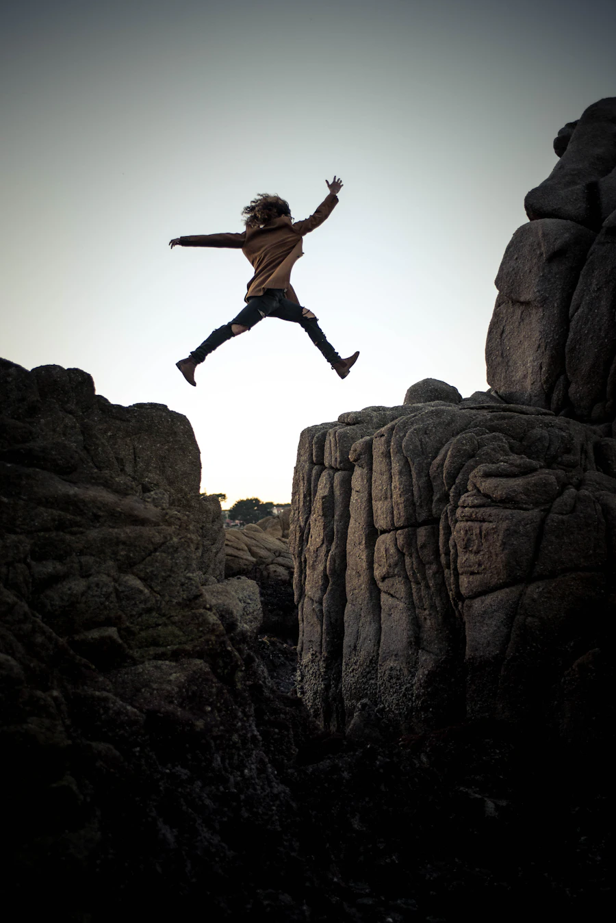 Don’t Look Down | person jumping on big rock under gray and white sky during daytime