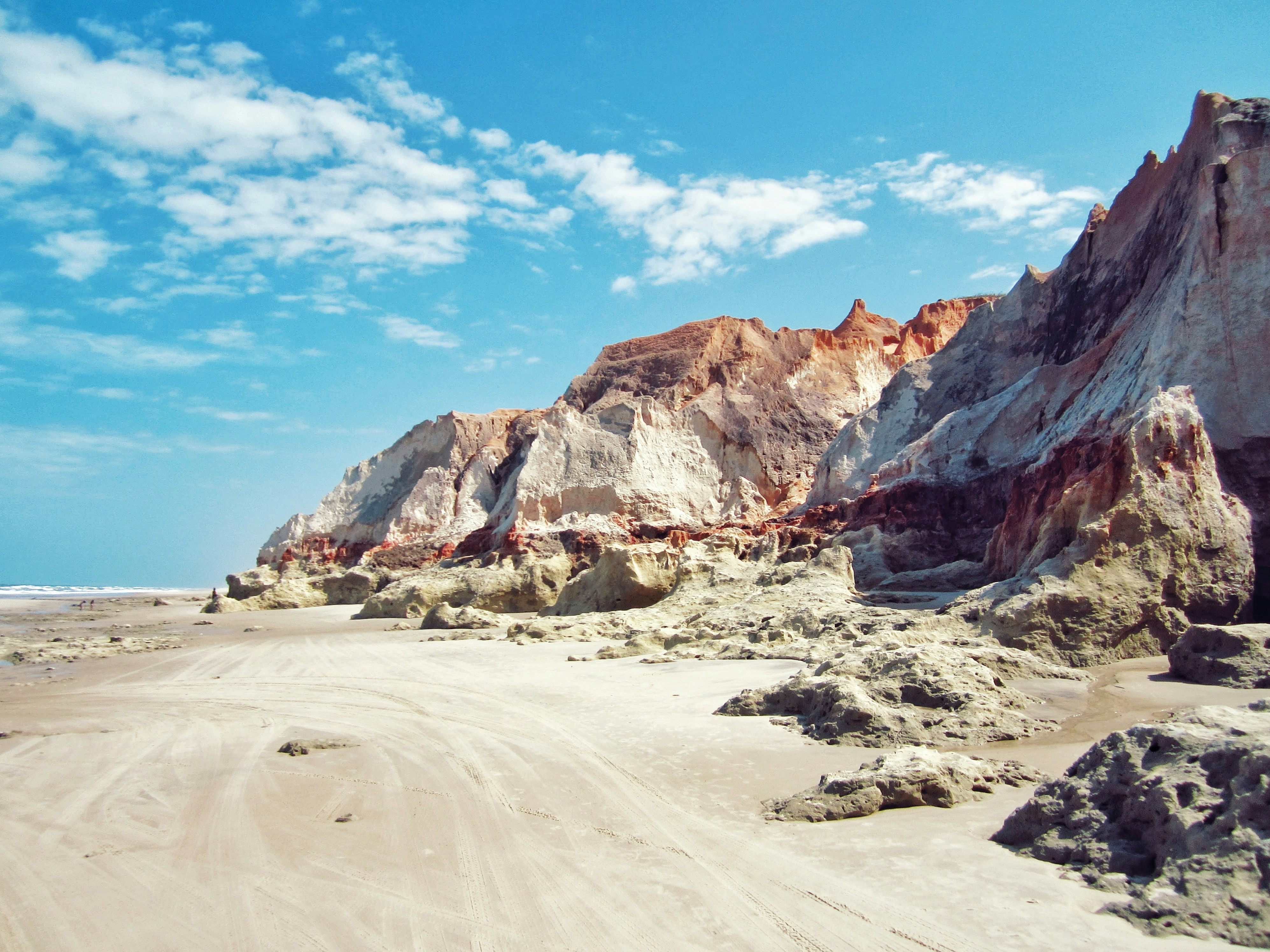 Vibrant cliffs reveal layers of sediment on a sandy beach under a bright blue sky.